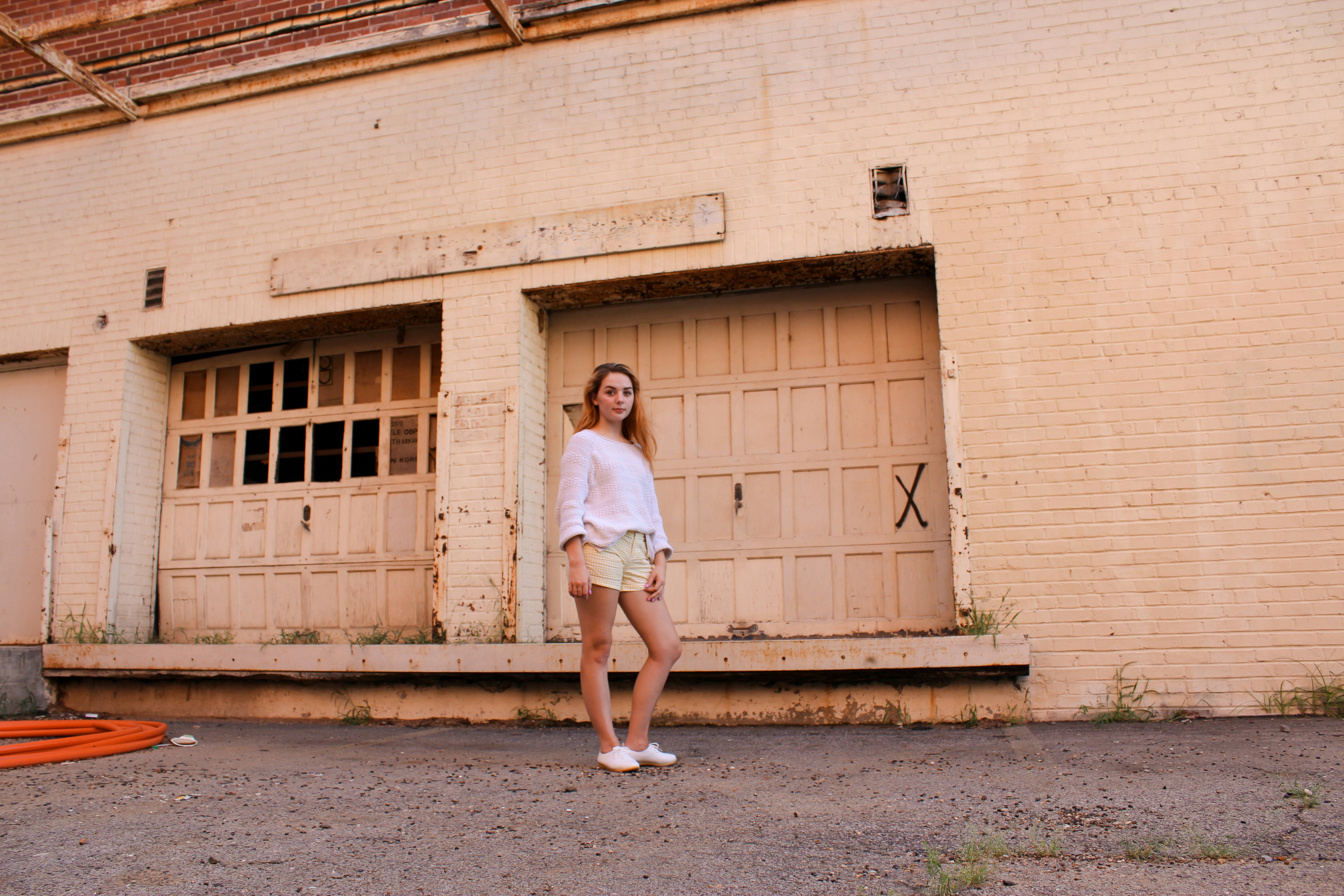 Person standing in front of a weathered, orange-painted building with closed garage doors.