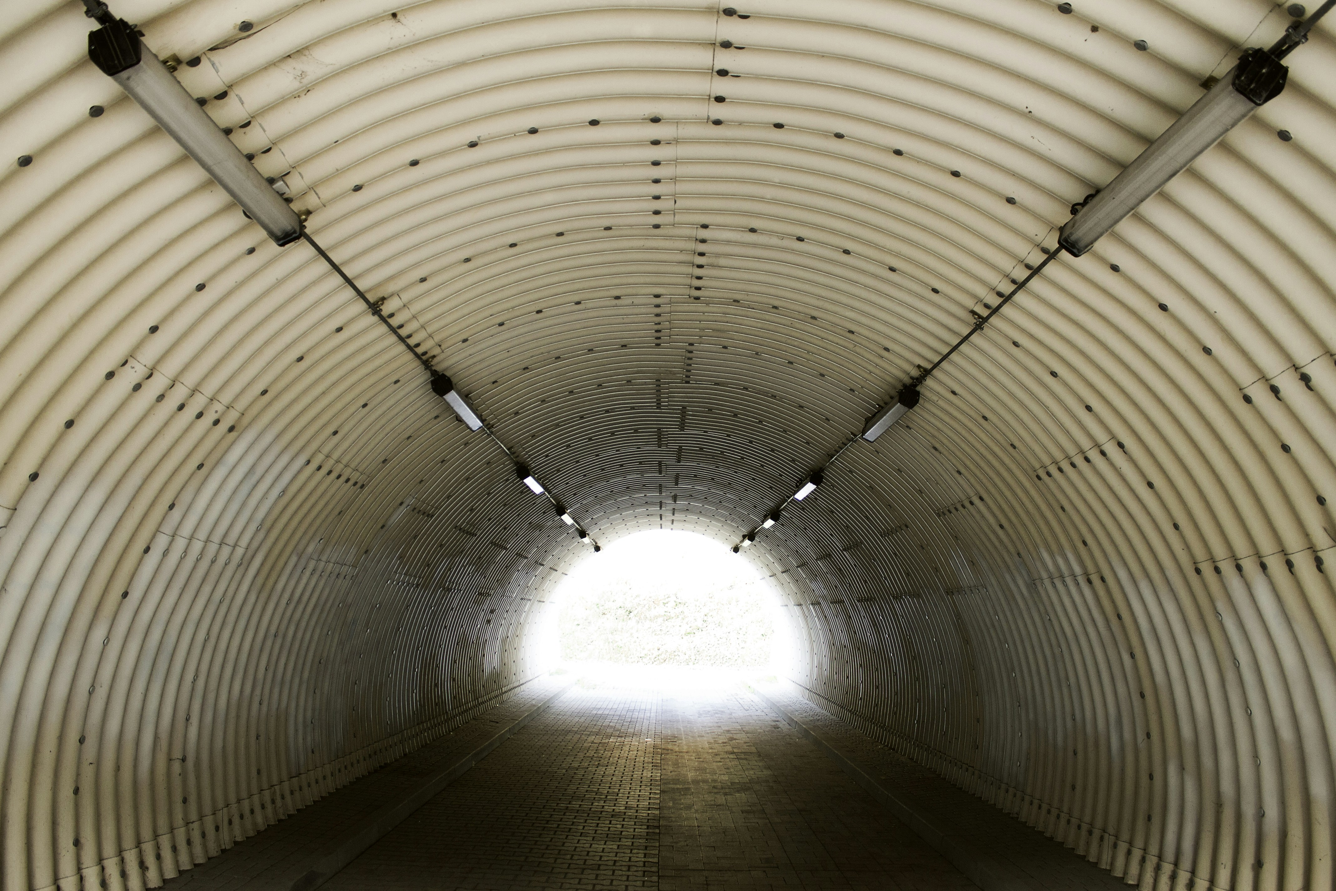 A well-lit tunnel with curved walls leading to a bright exit, showcasing the interplay of light and shadow.