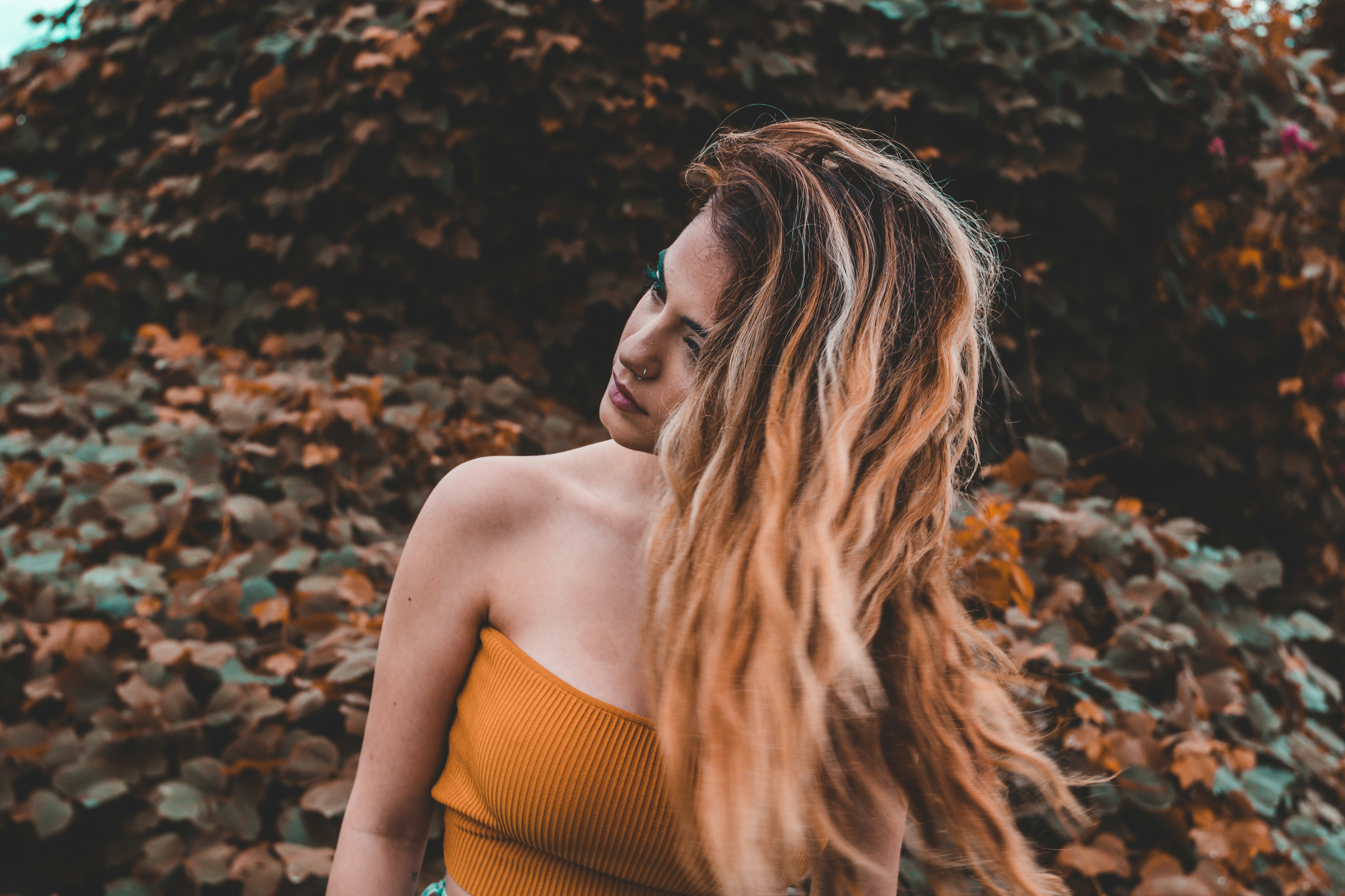 Woman with long hair stands before a backdrop of autumn leaves.