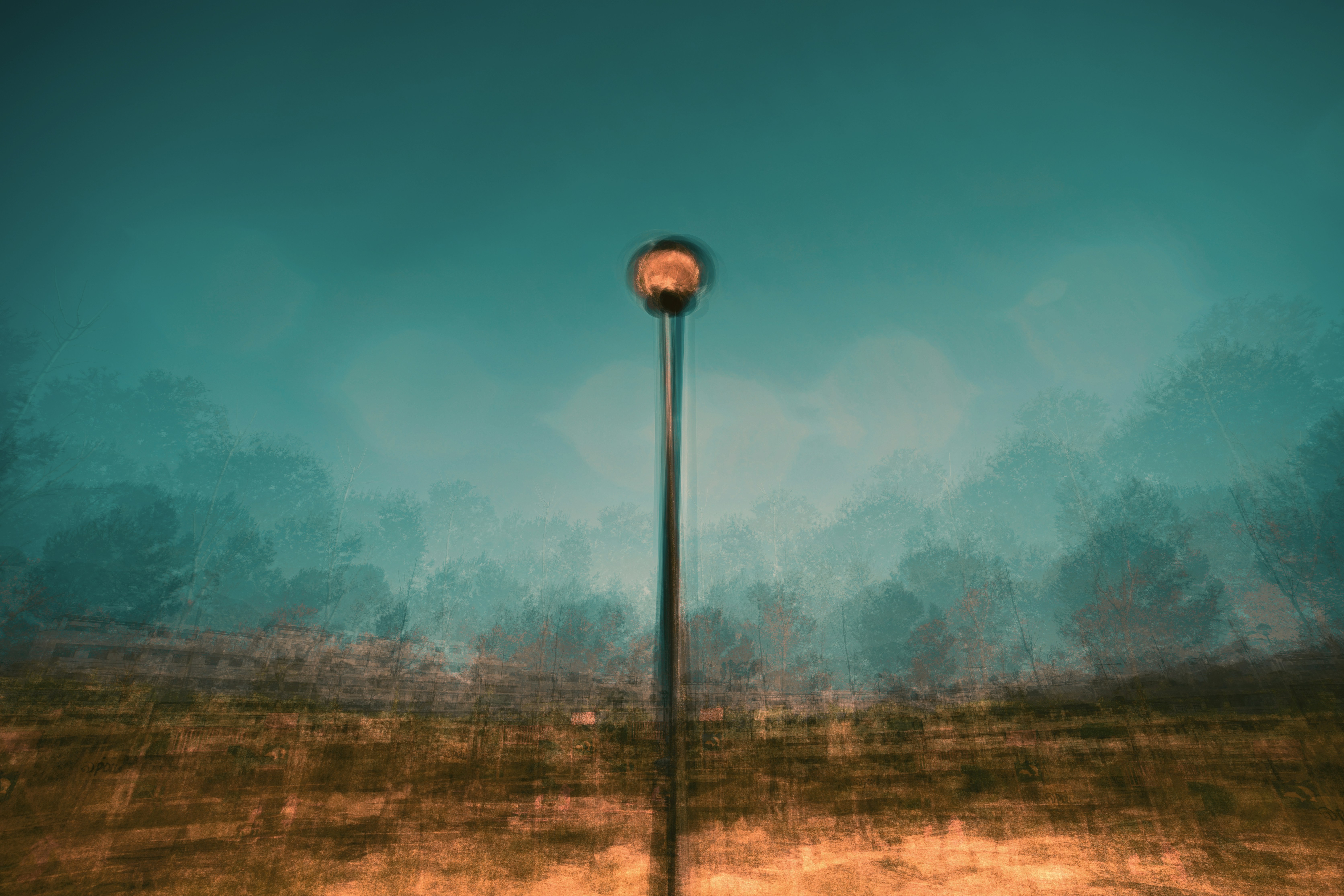 A solitary street lamp stands against a blurred backdrop of trees, evoking a sense of isolation and tranquility.