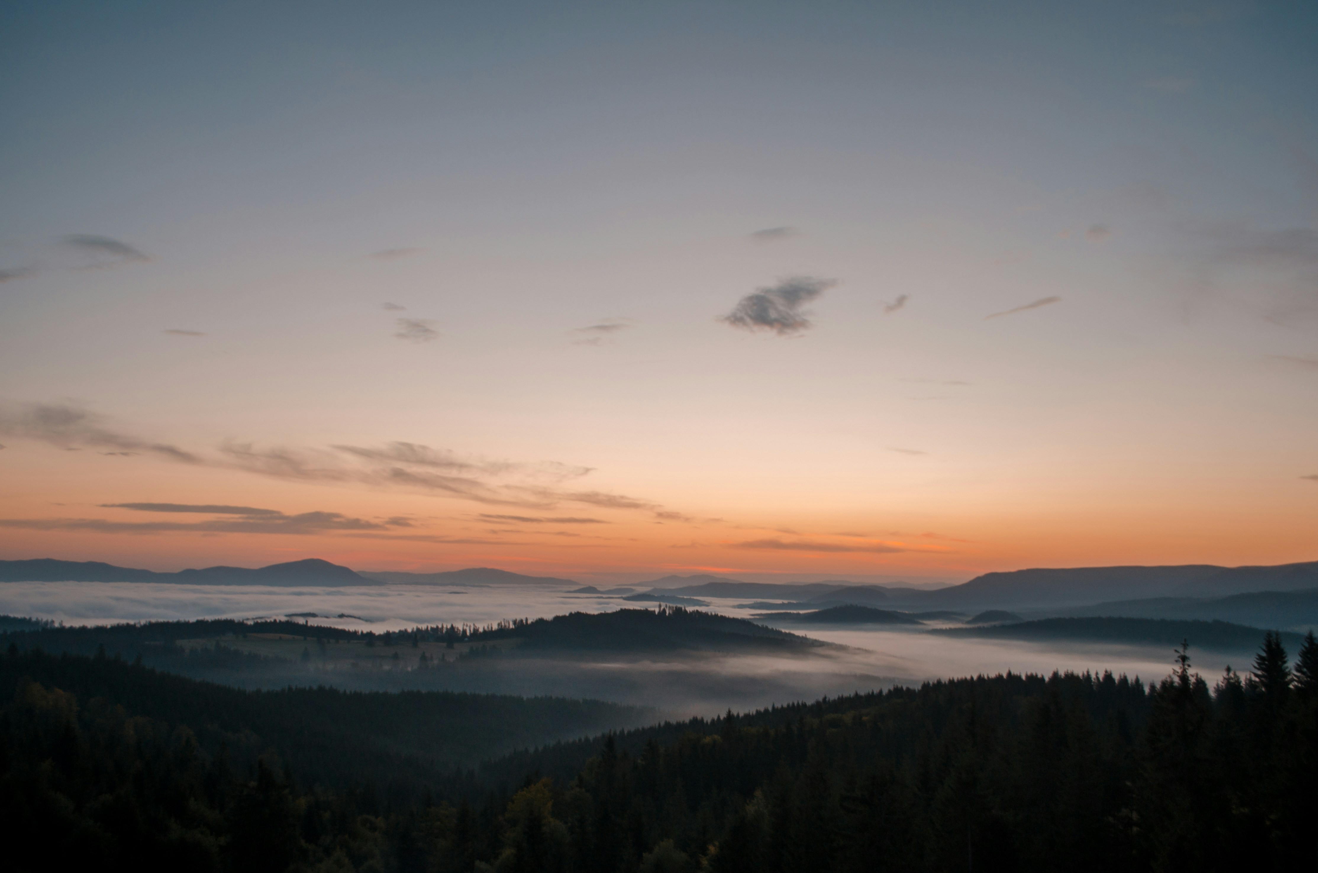 Sunrise over rolling hills shrouded in morning mist with a soft orange and blue sky.