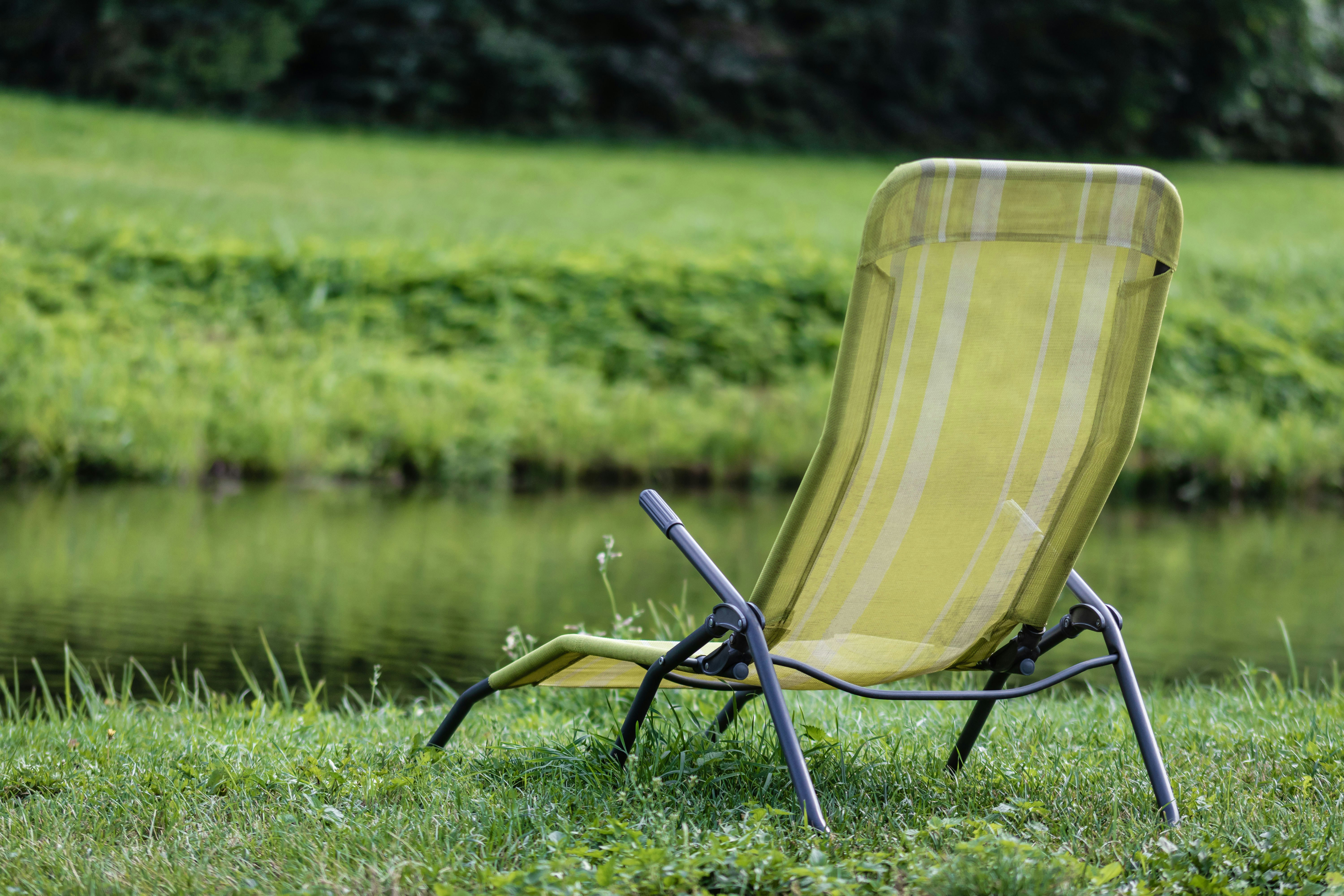 Yellow sunbed on grassy bank beside a serene pond.