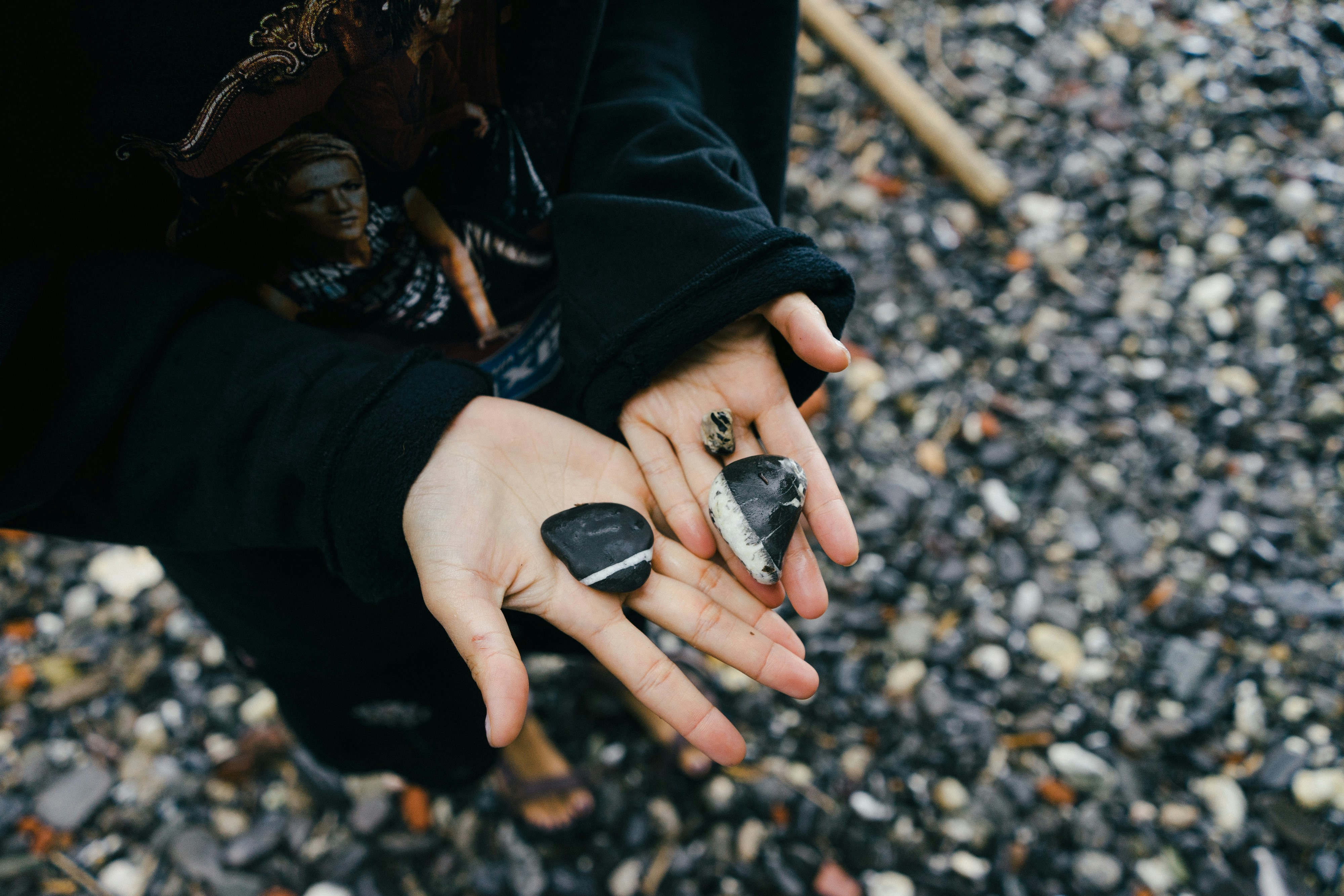 Hands holding unique stones against a backdrop of pebbles, showcasing the beauty of natural materials.
