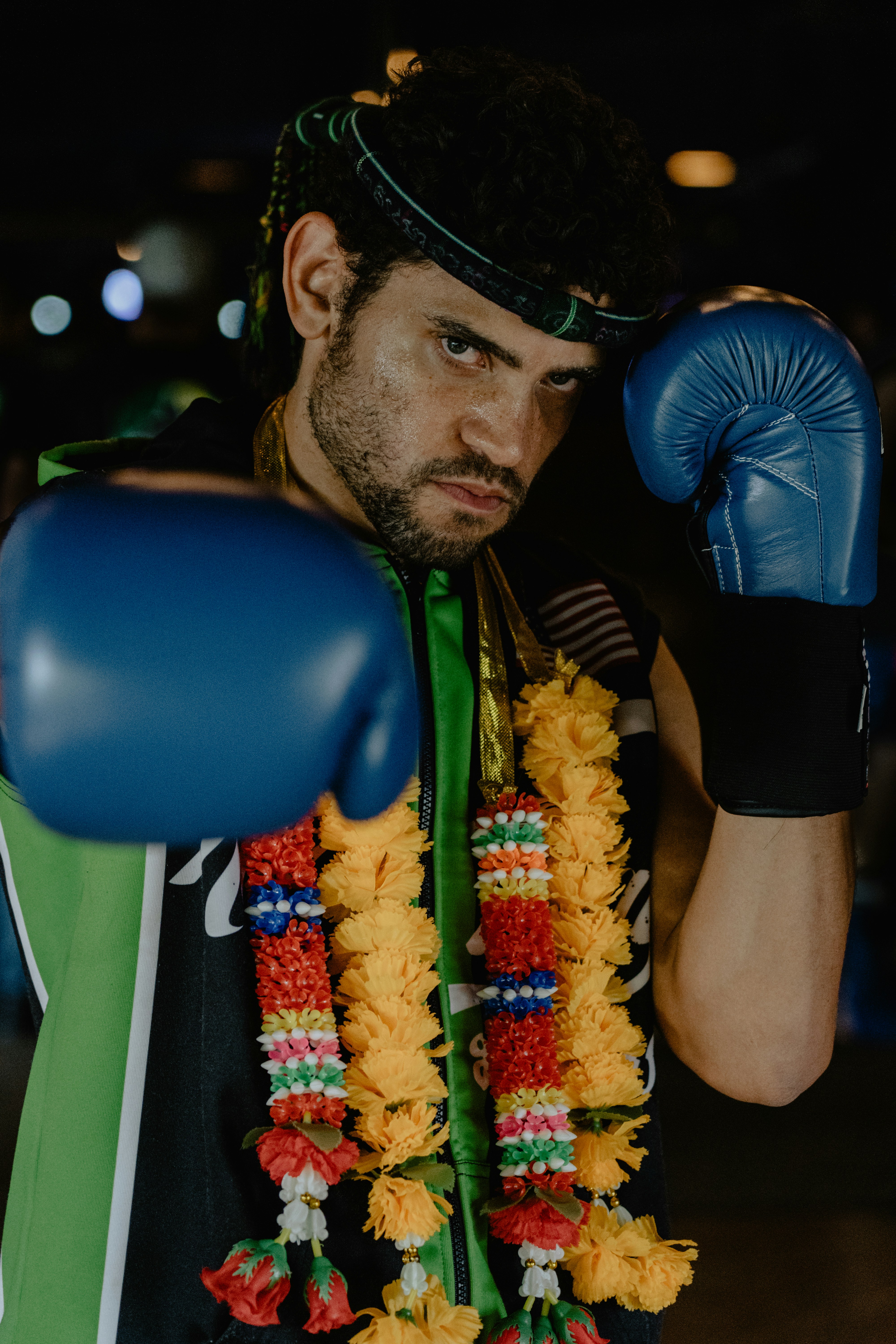 Boxer adorned with floral garlands and blue gloves, exuding determination and focus before a match.