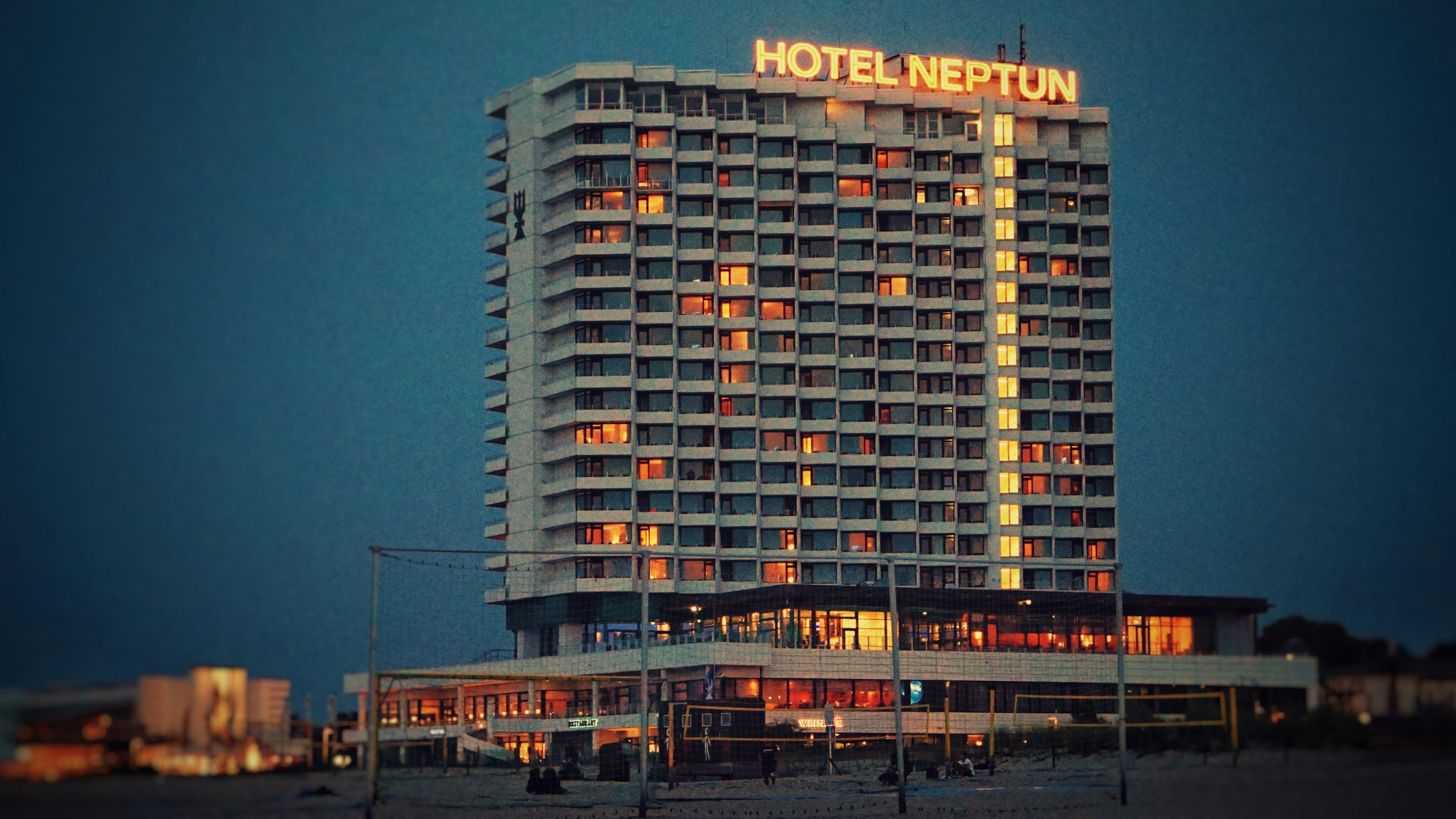 Modern hotel with illuminated windows and signage against a twilight sky, showcasing architectural design and ambiance.