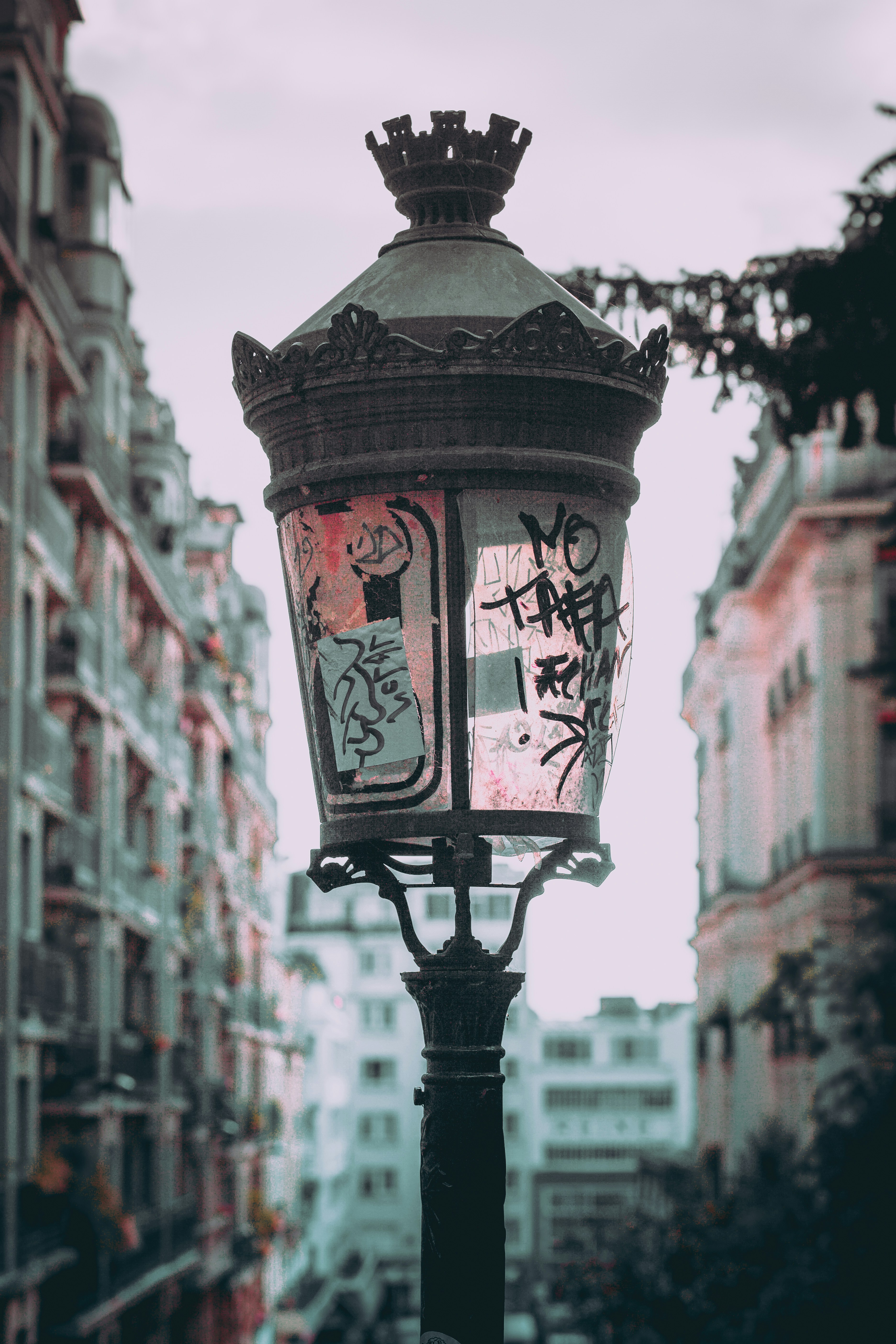 Vintage street lamp adorned with graffiti stands amidst urban architecture, highlighting the contrast between old and new. 