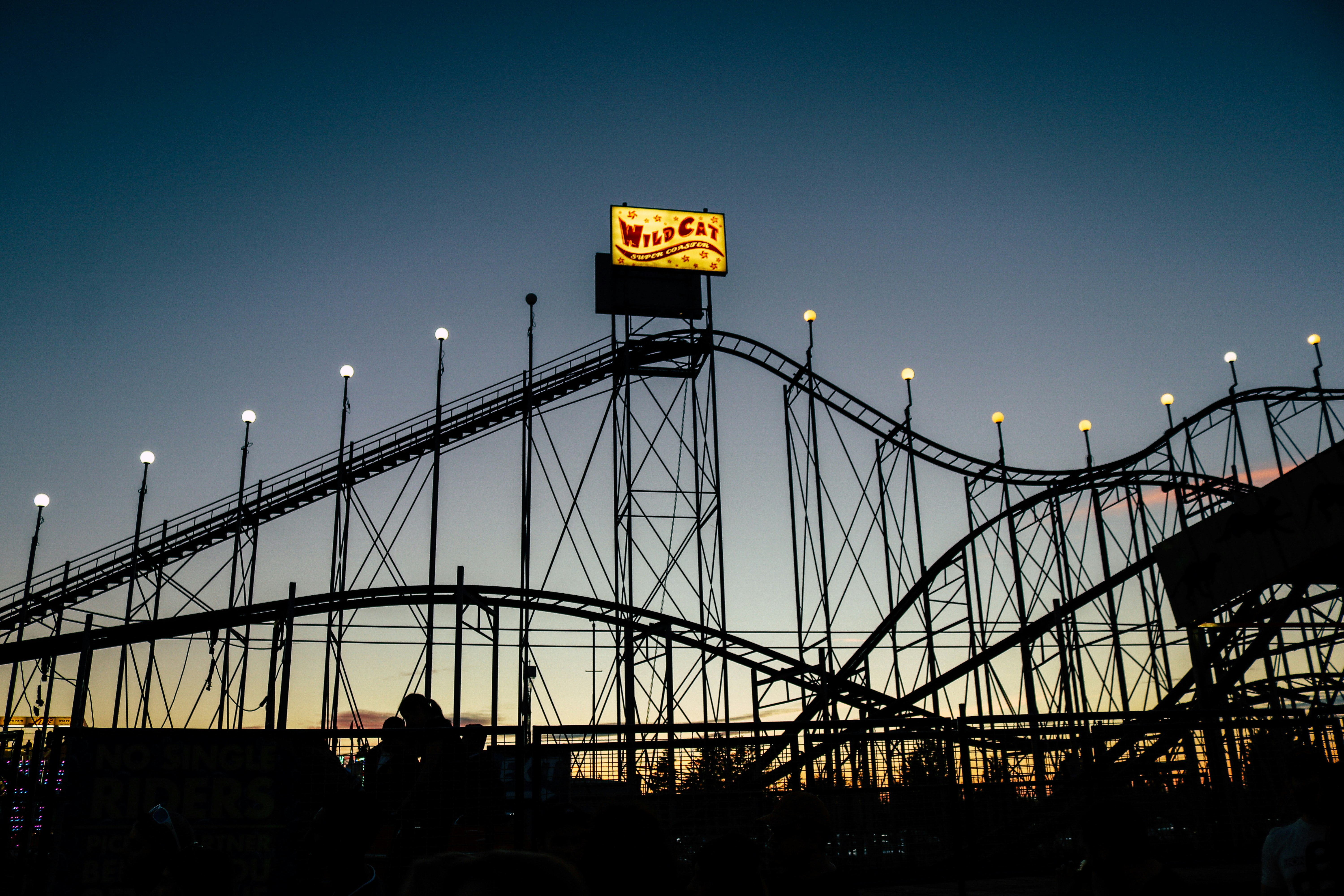 Silhouetted roller coaster against a twilight sky with a lit sign and visible track details.