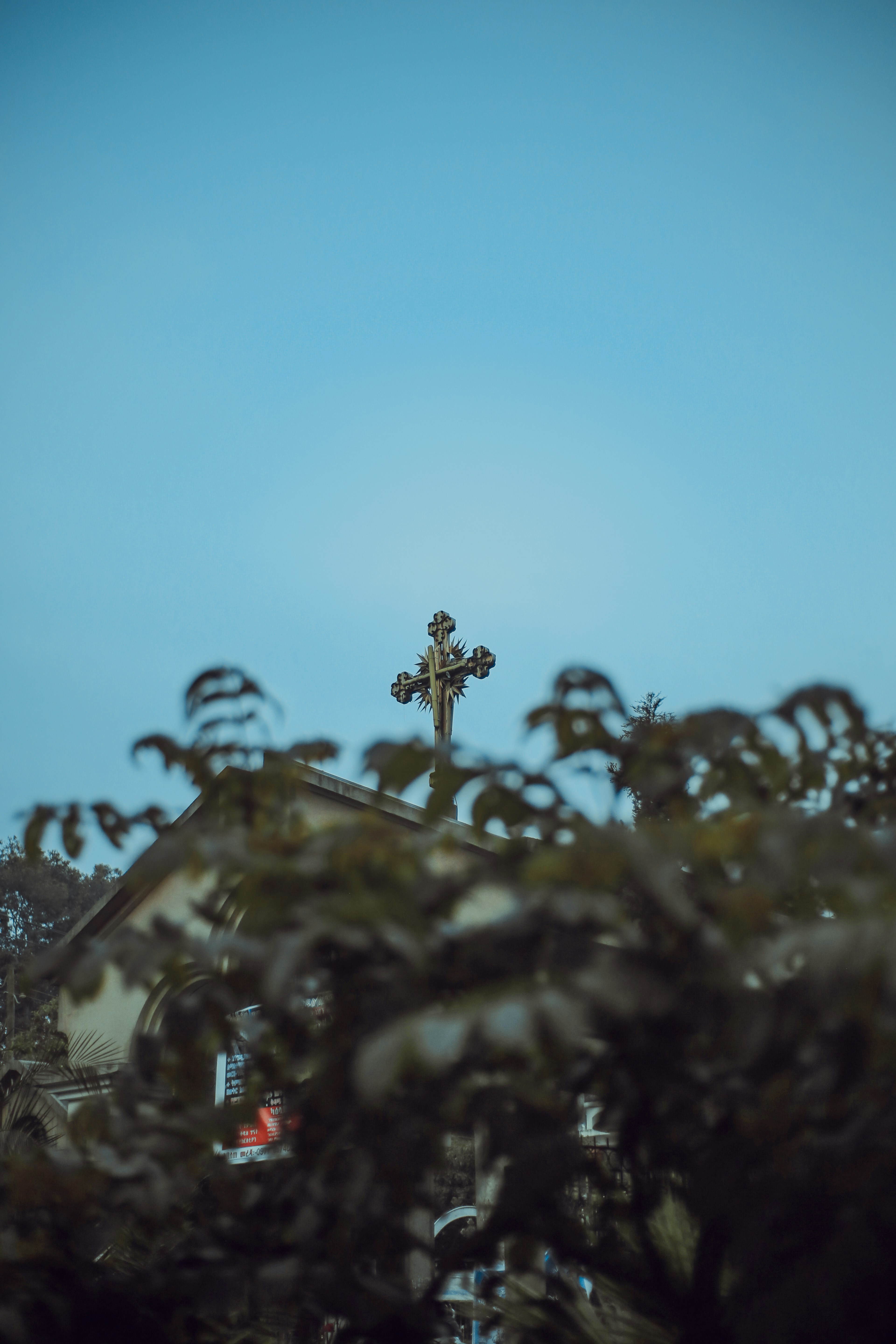 Cross Above the Roof: A Quiet Chapel Framed by Foliage Under a Calm Azure Sky