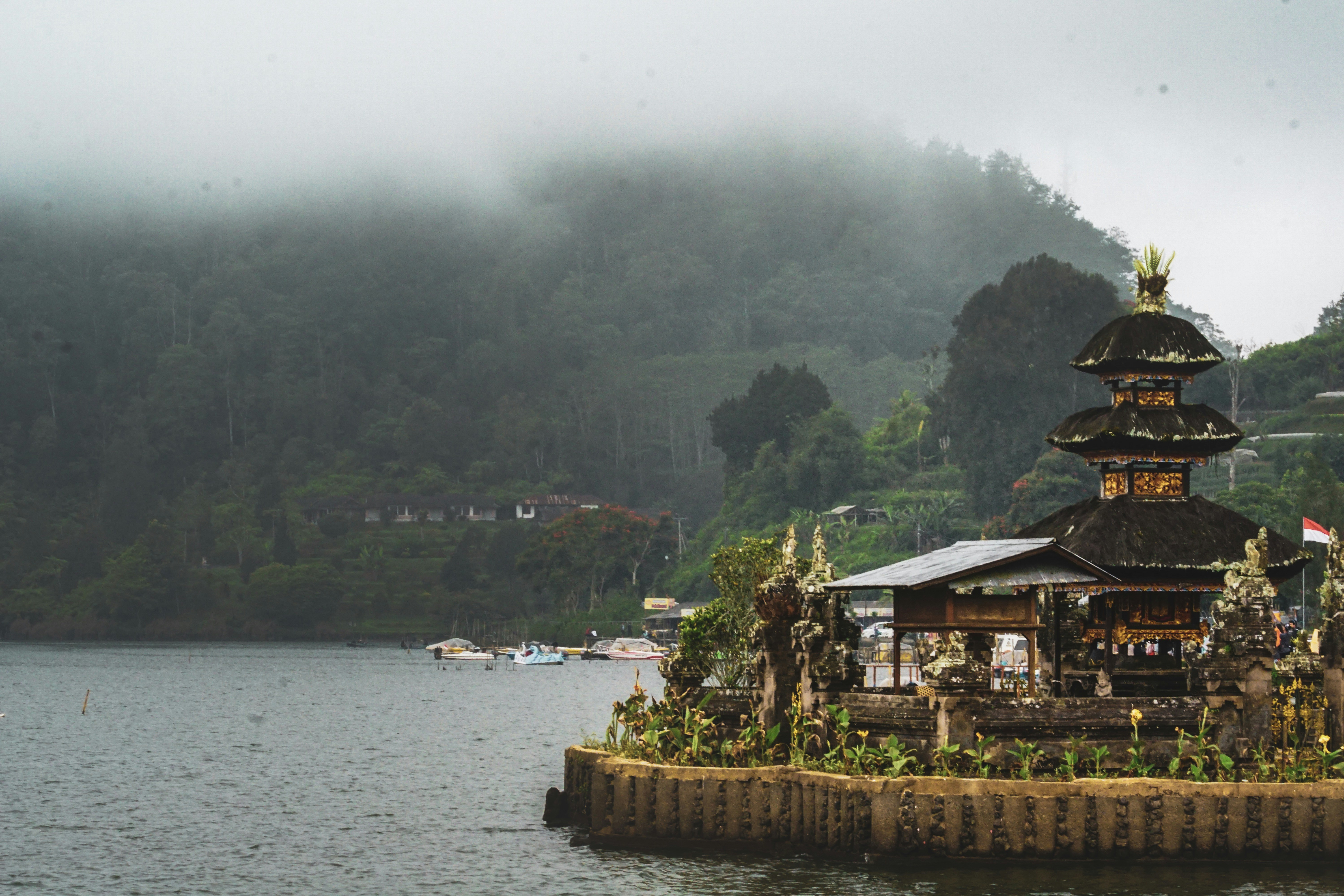 Traditional Balinese temple surrounded by lush greenery, reflecting on the tranquil lake under a misty sky.