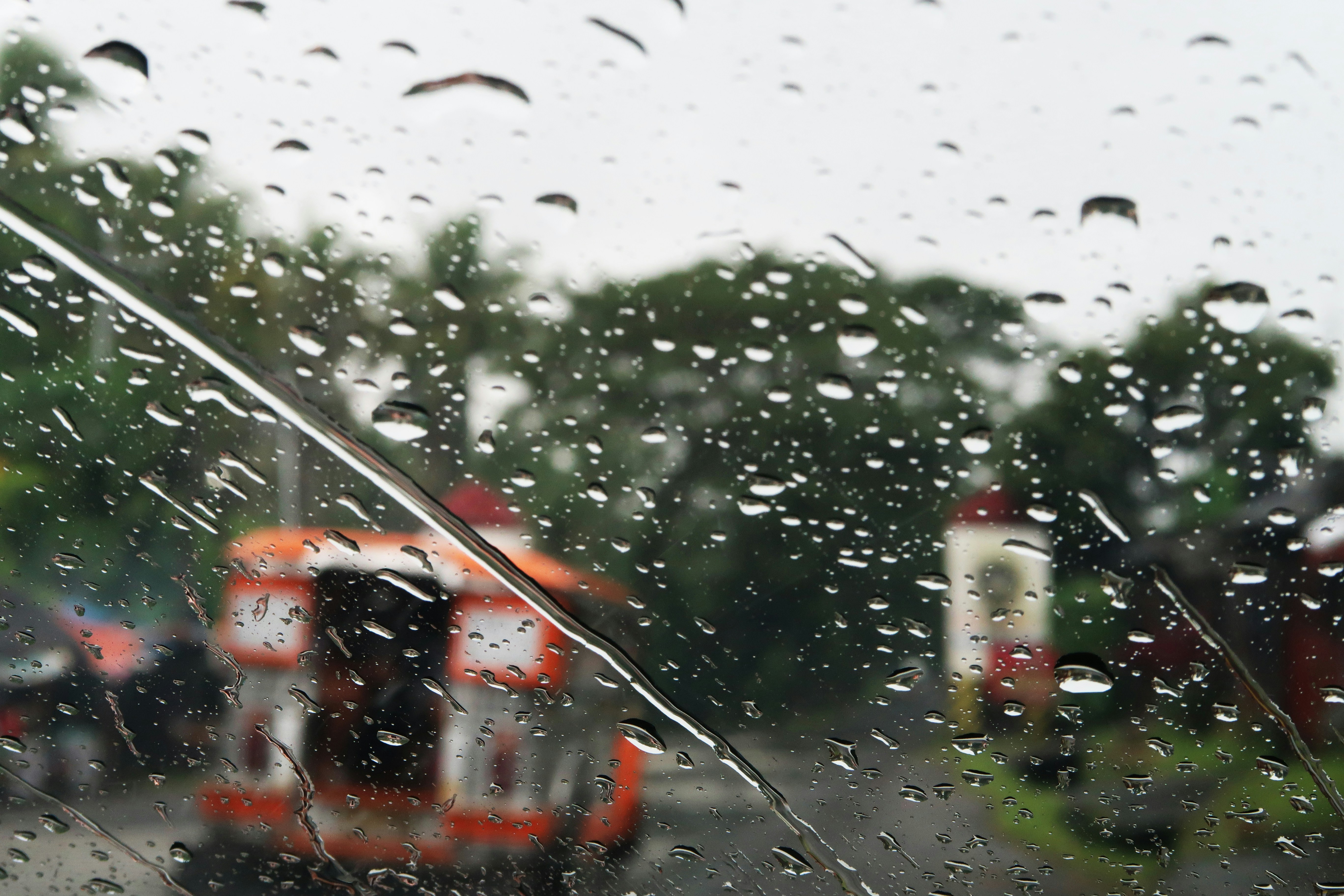 Raindrops cling to a car window, blurring the vibrant colors of a jeepney and lush greenery in the background.