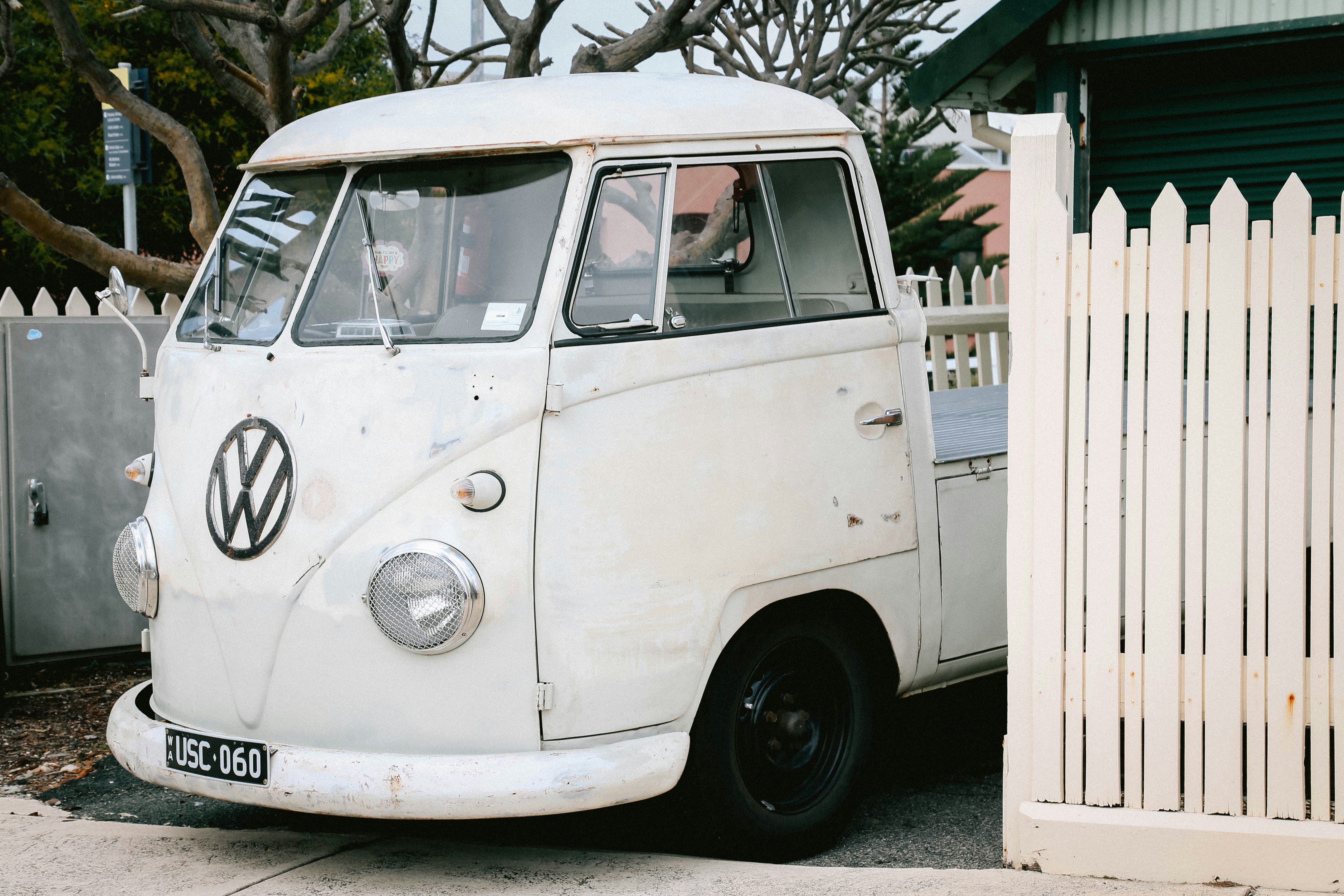 Patina on Wheels: A Weathered VW Van by a Pale Picket Fence