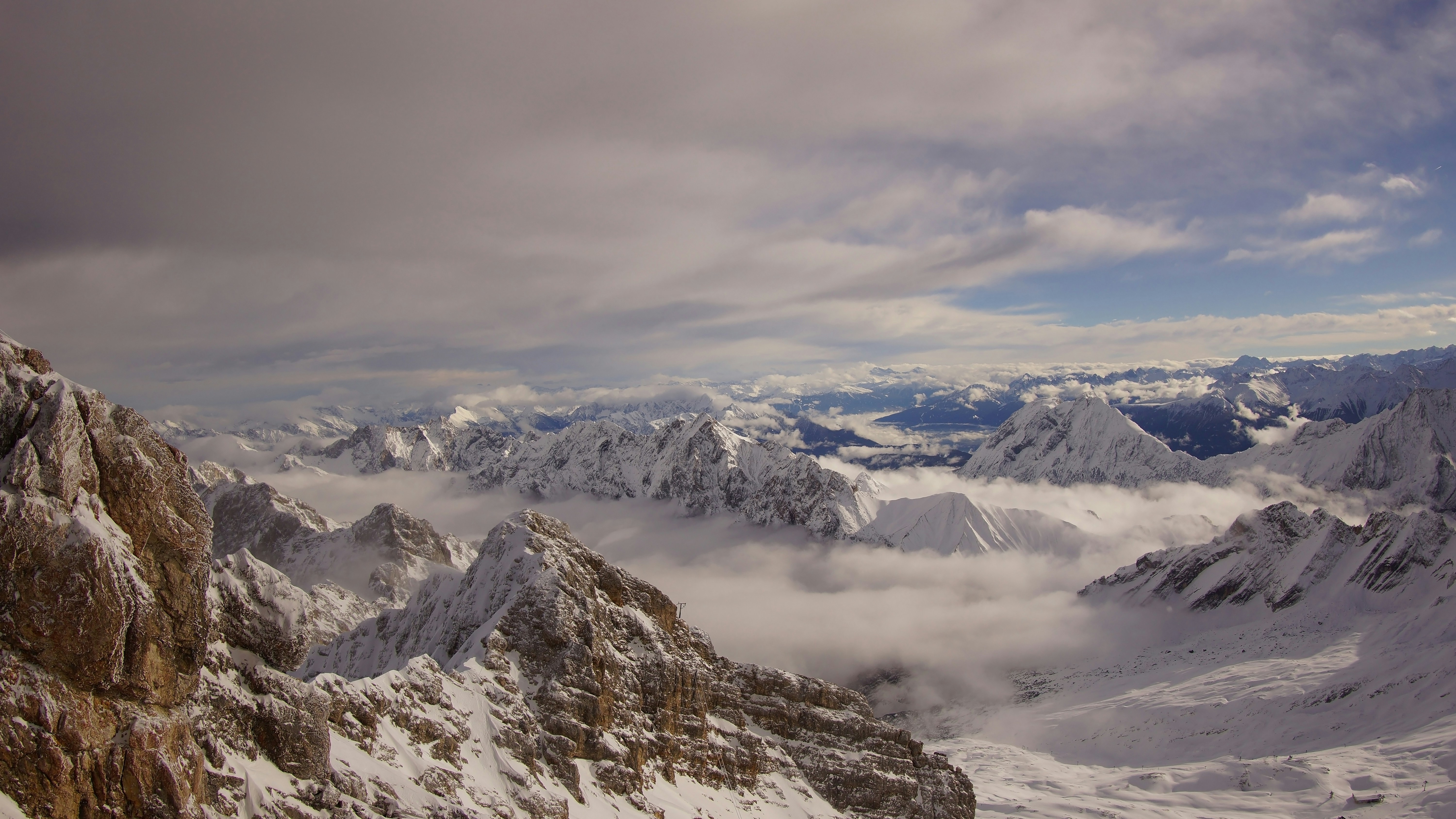 Snow-covered mountain peaks beneath a cloudy sky with scattered sunlight.