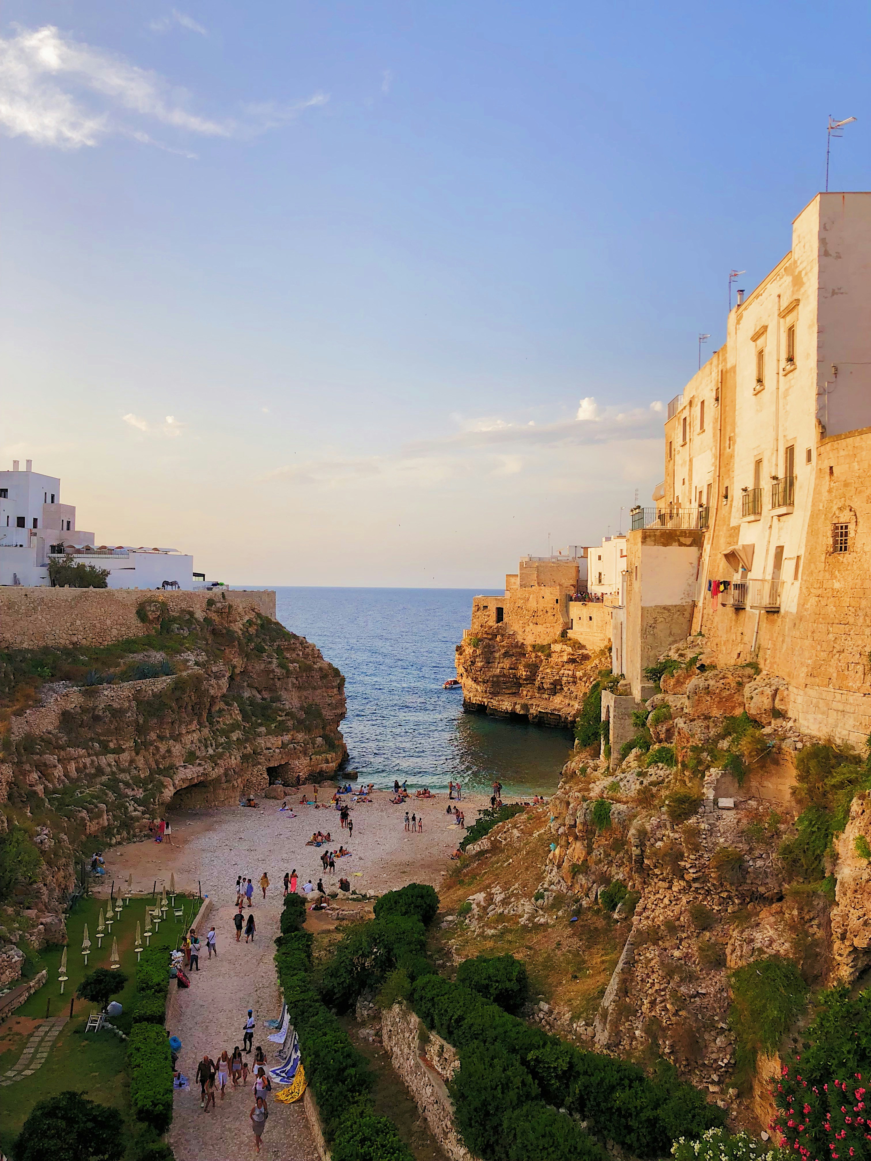 A picturesque coastal scene featuring a sandy beach surrounded by rocky cliffs and charming buildings at sunset.