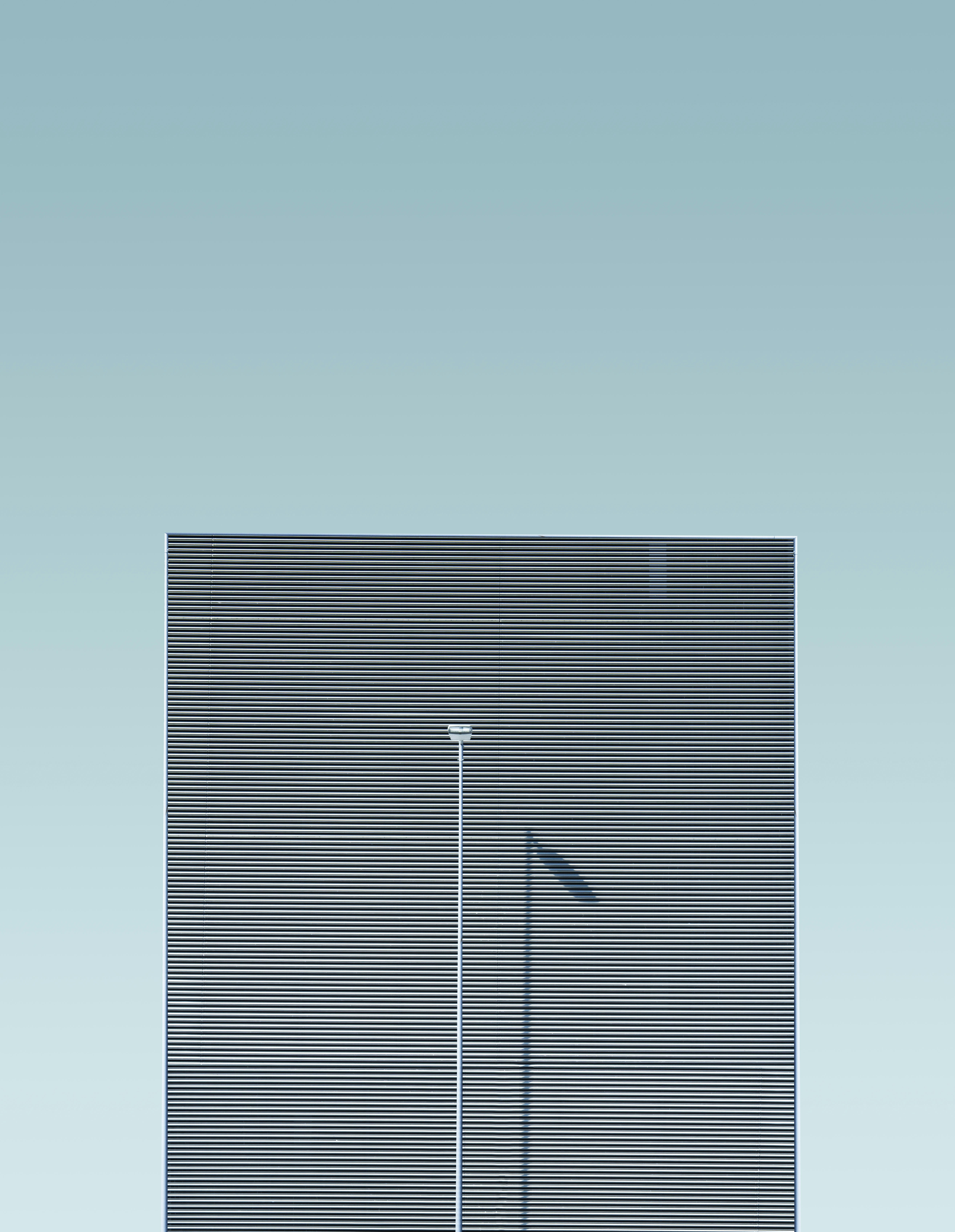 A minimalist architectural facade featuring horizontal lines and a solitary streetlight against a clear sky.
