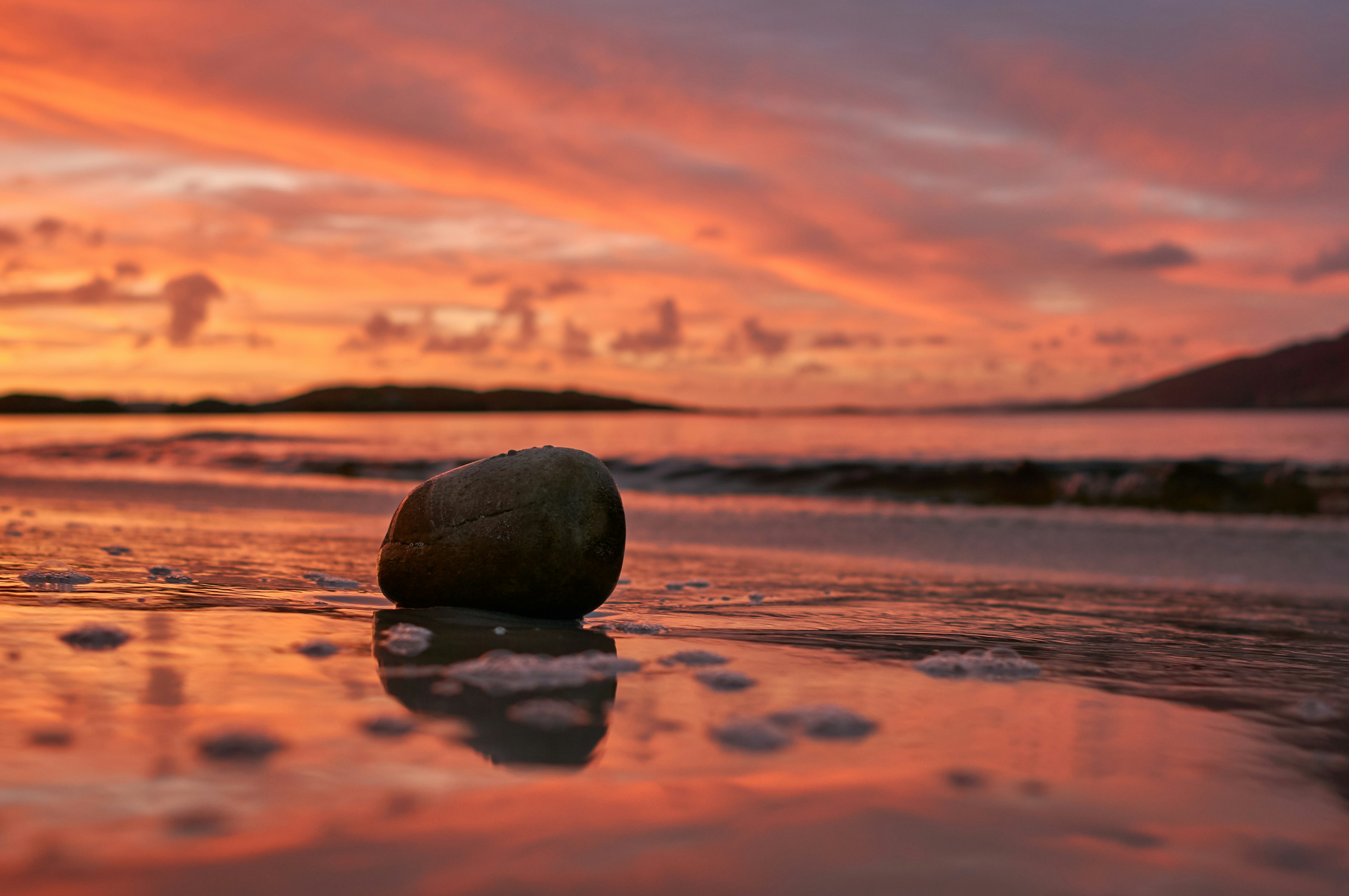 A solitary stone rests at the shoreline as ember skies glow