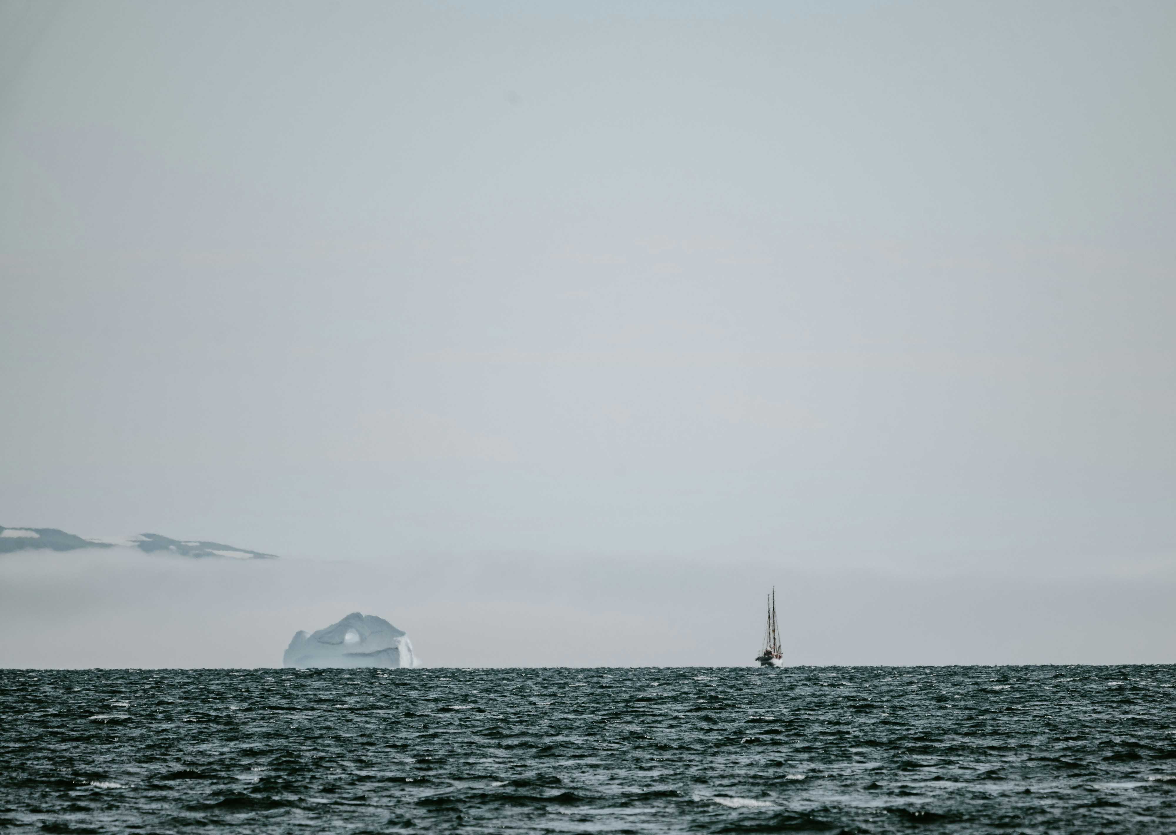 Iceberg on a pale horizon, a lone sail crossing quiet seas