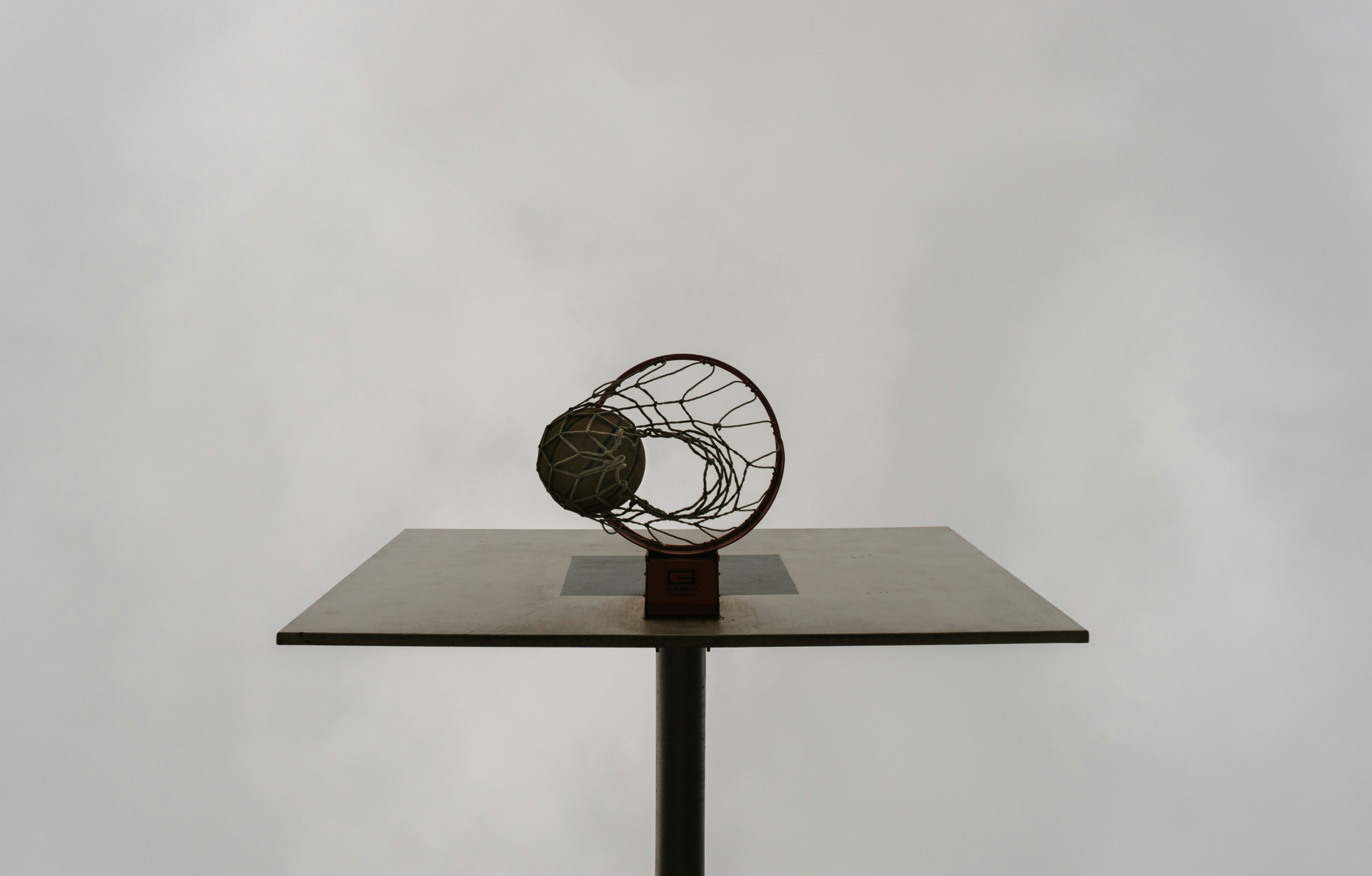 Basketball poised in mid-air above a hoop against a cloudy sky.