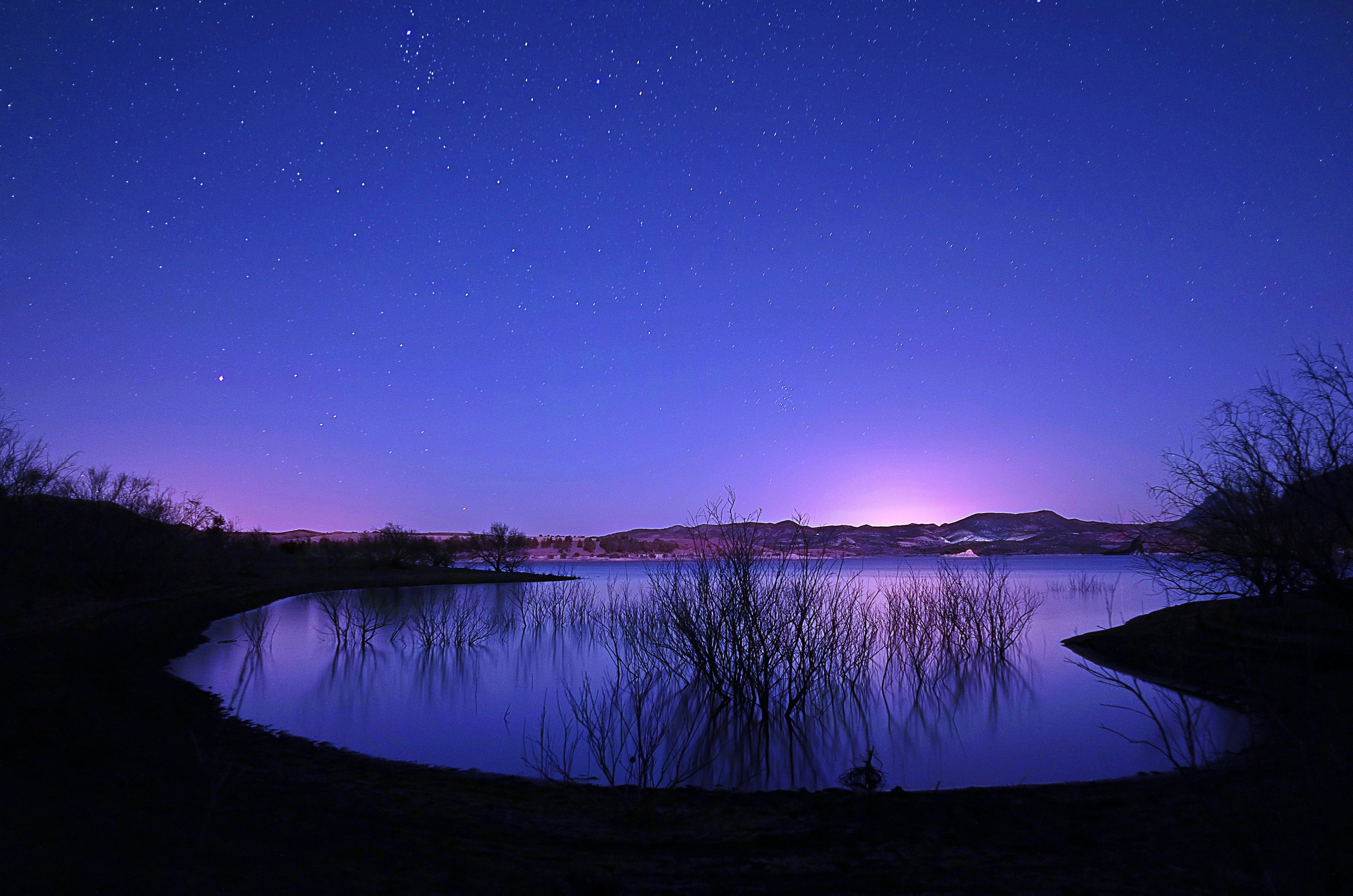 Horizon Glow Over a Glassy Lake Beneath a Star-Pattered Sky