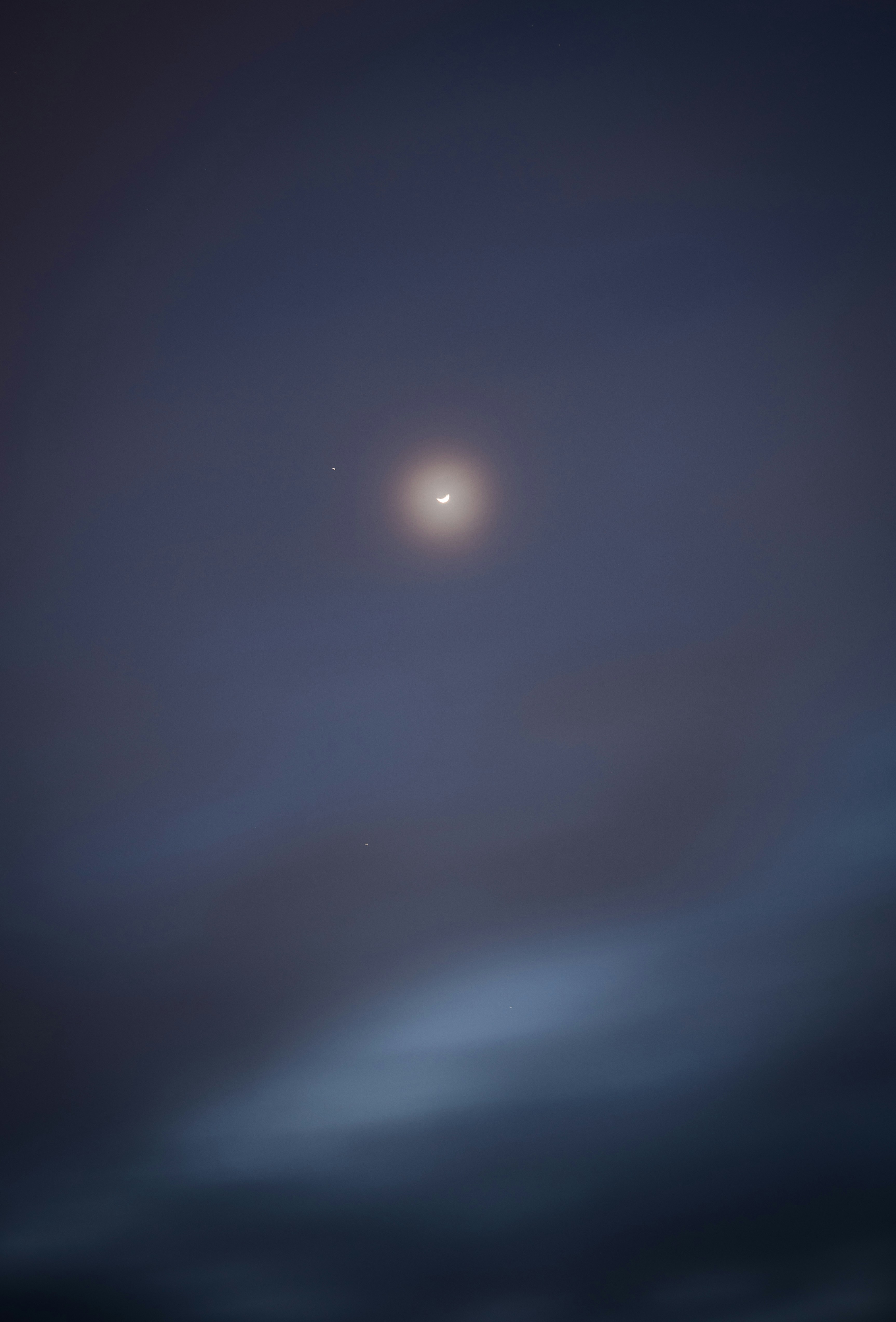A crescent moon surrounded by wispy clouds in a twilight sky, with faint stars twinkling nearby.