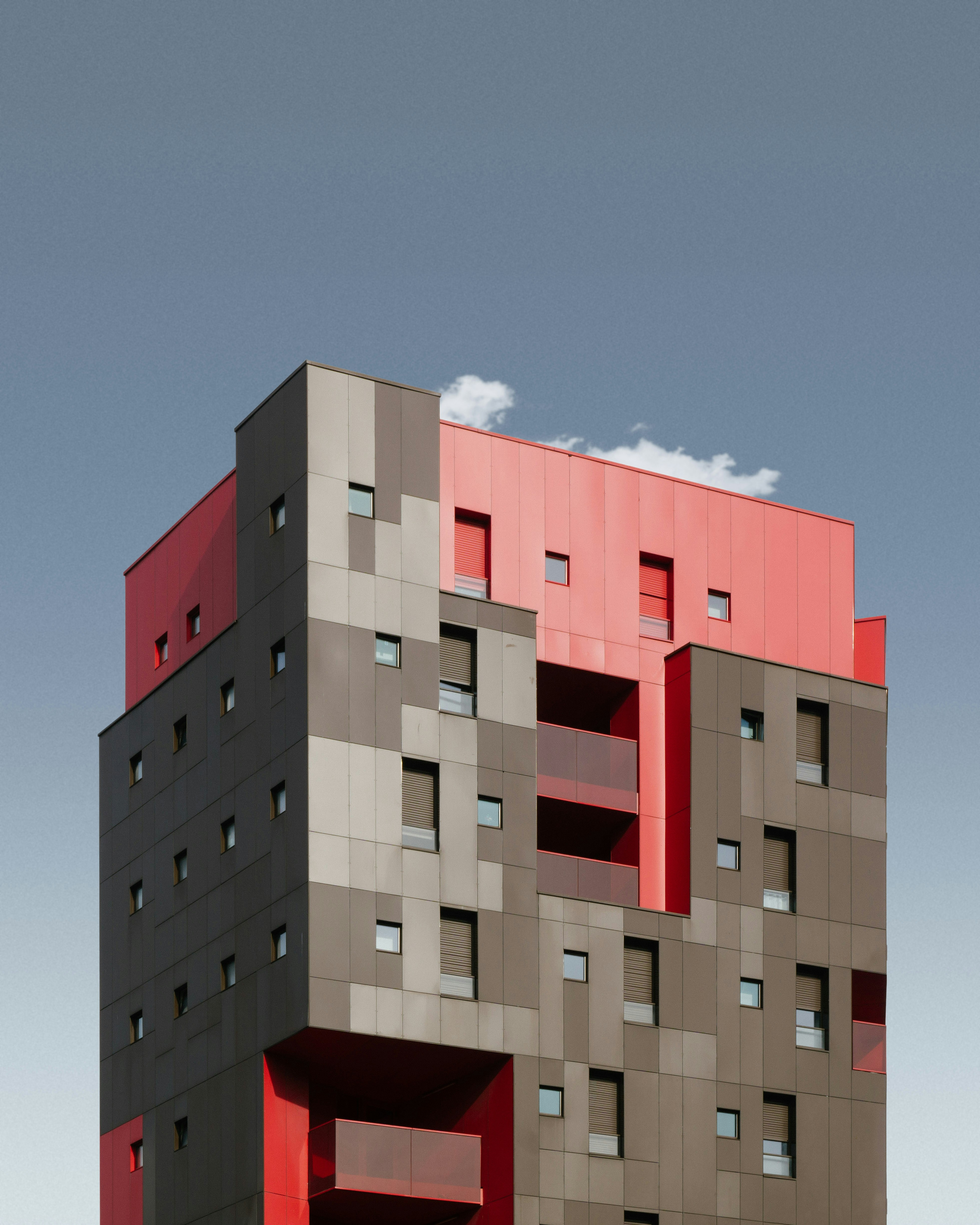 A contemporary building featuring a striking combination of red and gray panels with an intriguing geometric design. The structure showcases modern architectural elements.