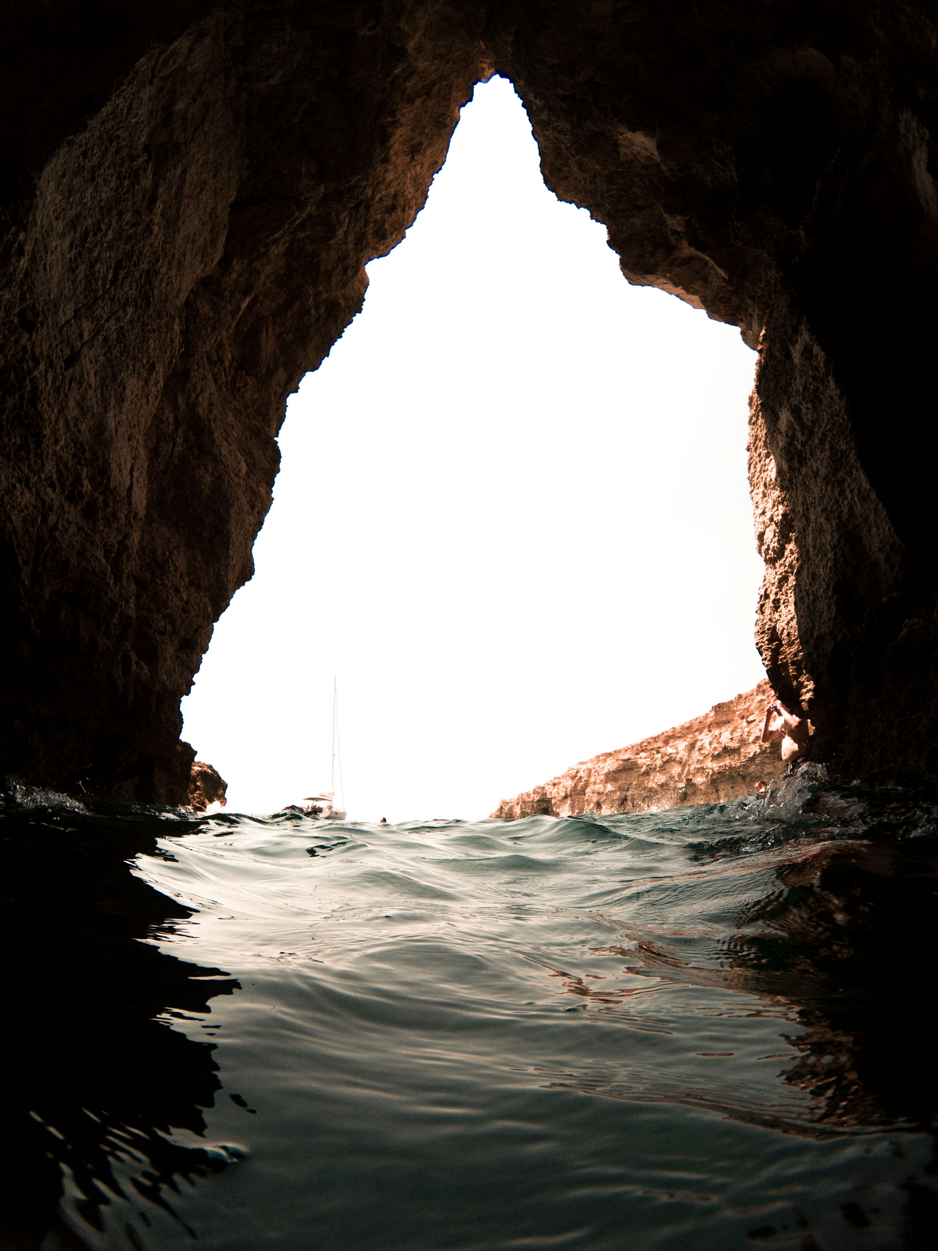 View through a rocky archway revealing a serene seascape beyond. The interplay of light and water creates a peaceful ambiance.