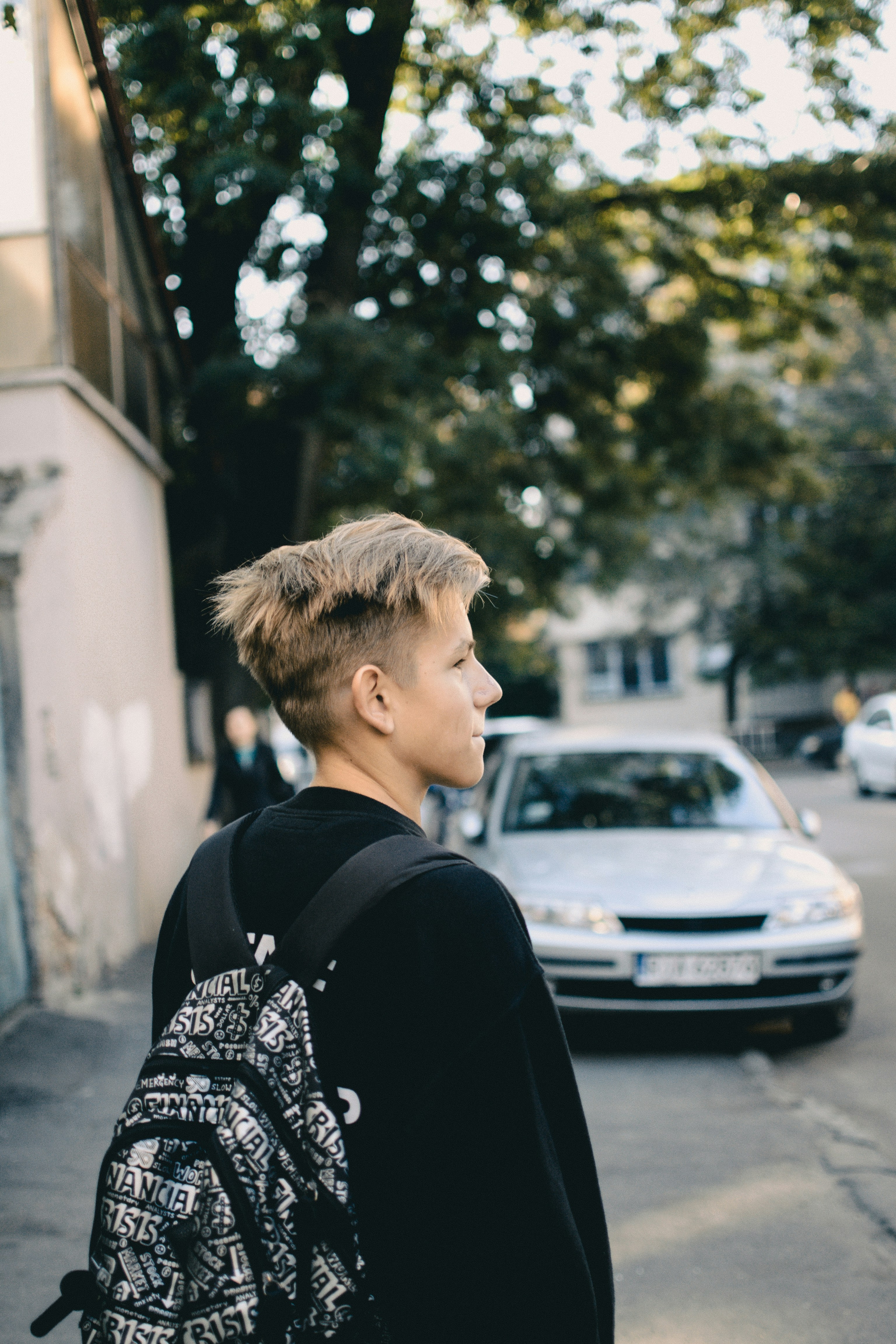 Young person walking down a city street, showcasing a casual urban atmosphere with a parked car in the background. 