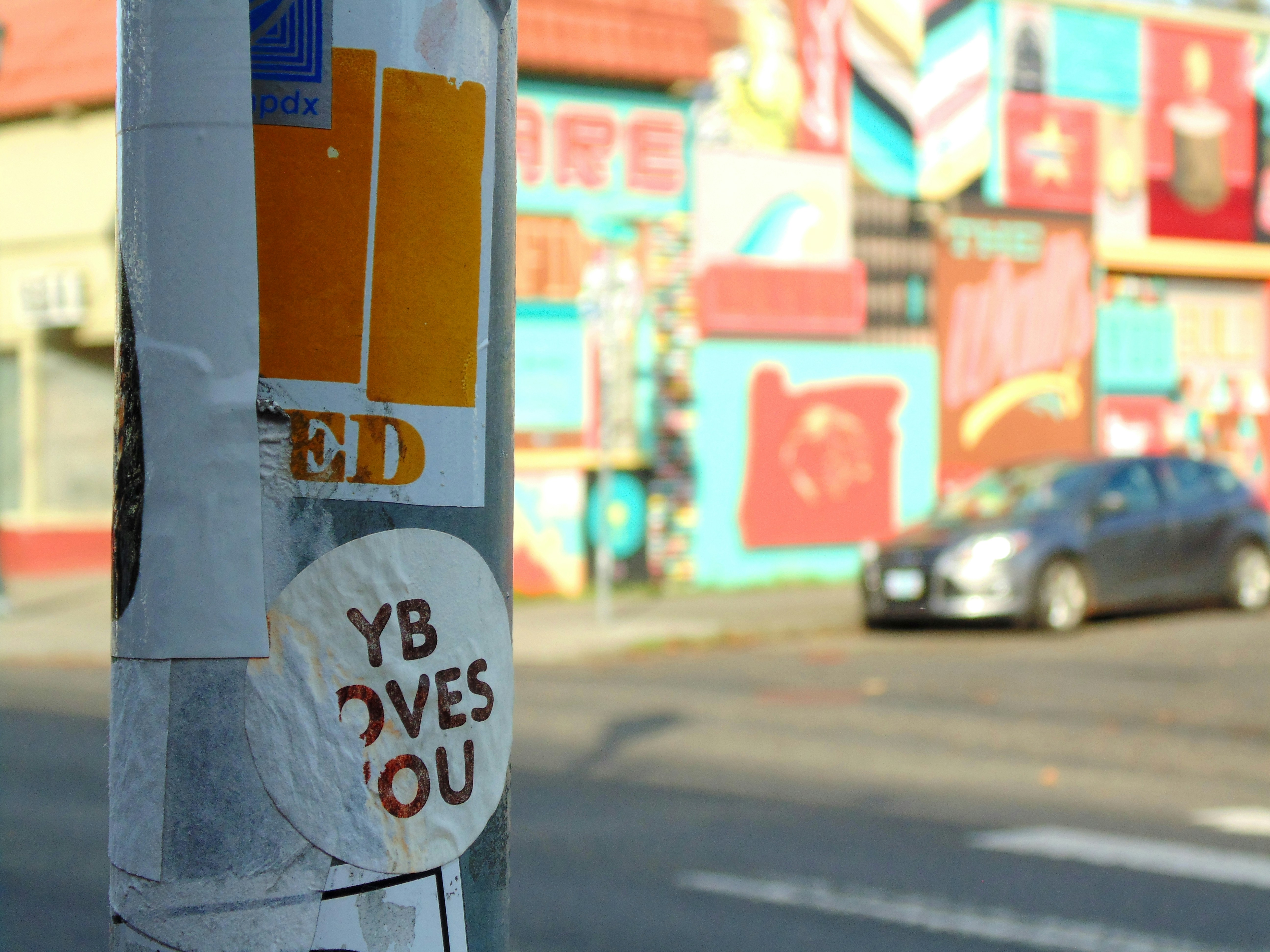 Sticker on a Weathered Pole Framing a Rainbow Street Wall