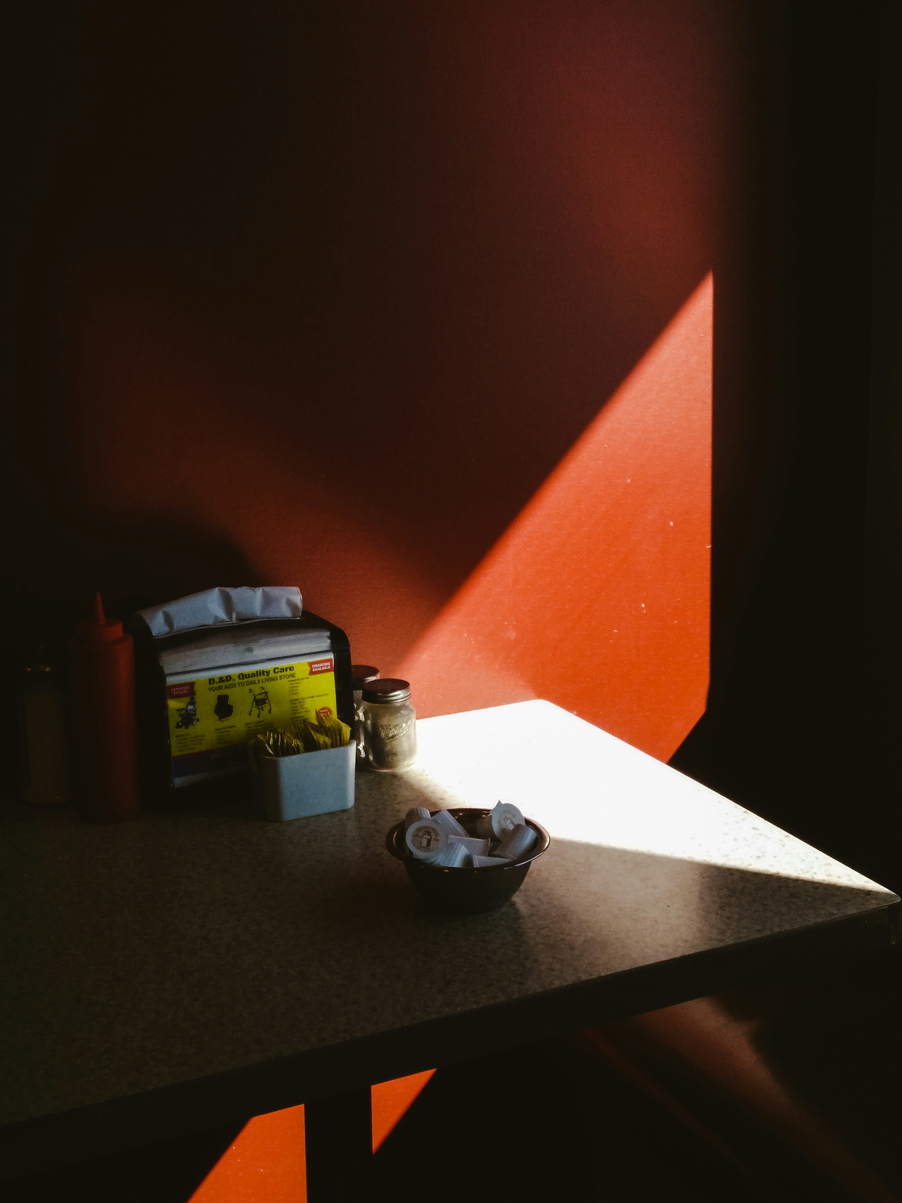 Warm tabletop still life photo featuring a bowl and condiment jars, with a diagonal sunbeam slicing across an orange wall.
