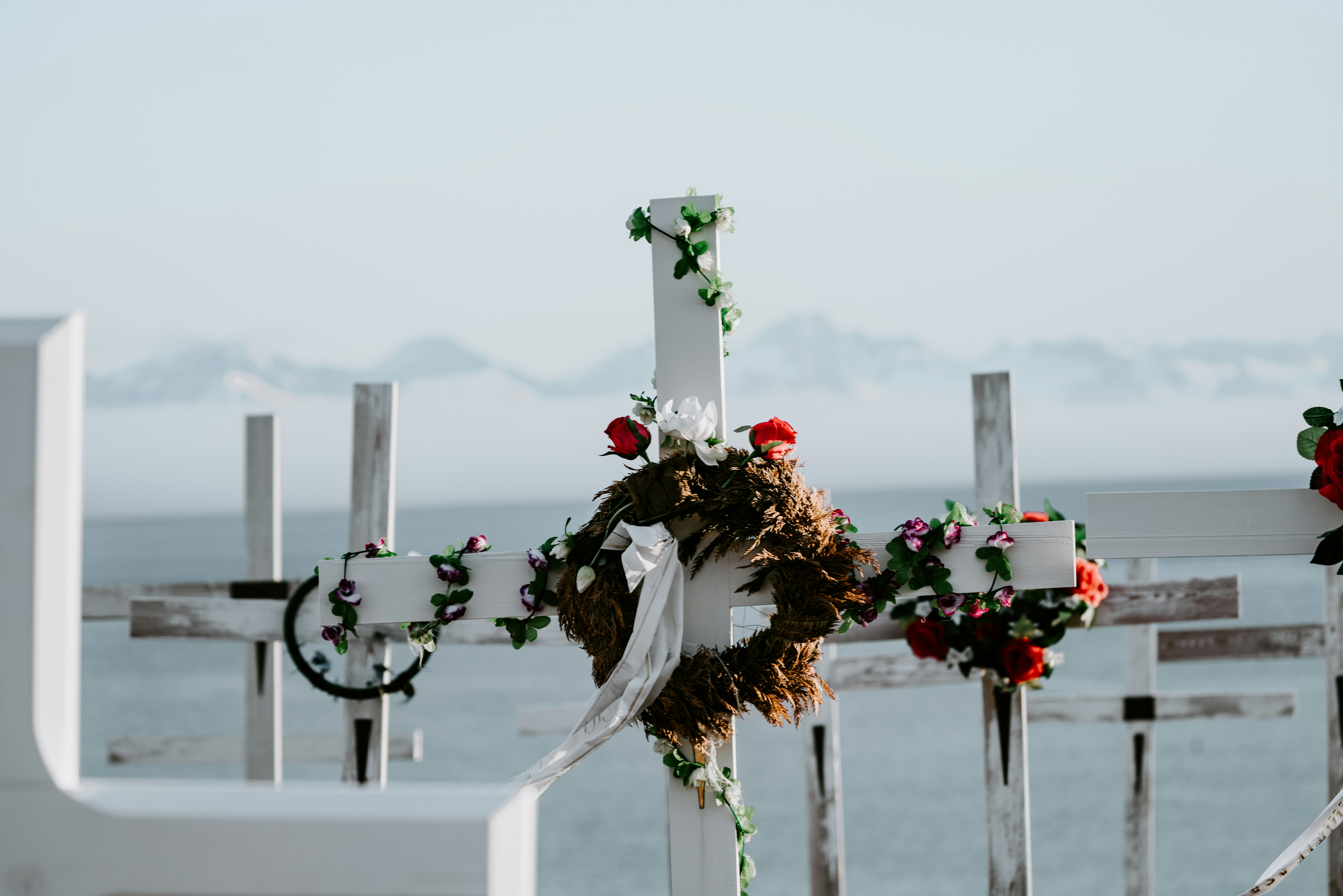 Seaside Memorial: A White Cross Adorned with Floral Wreaths Reaches Toward an Open Horizon