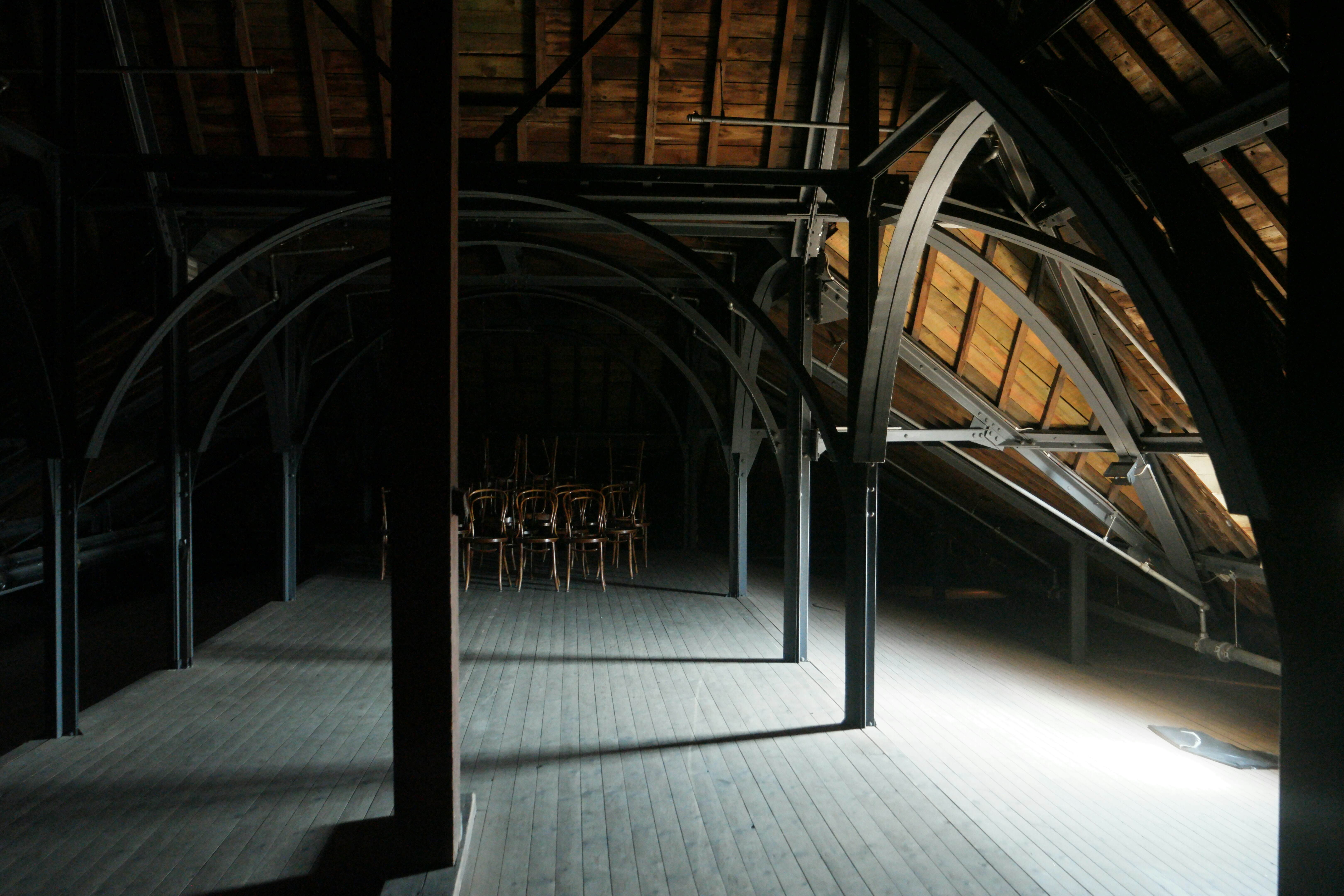 Dimly lit attic space with wooden beams and chairs, casting long shadows.
