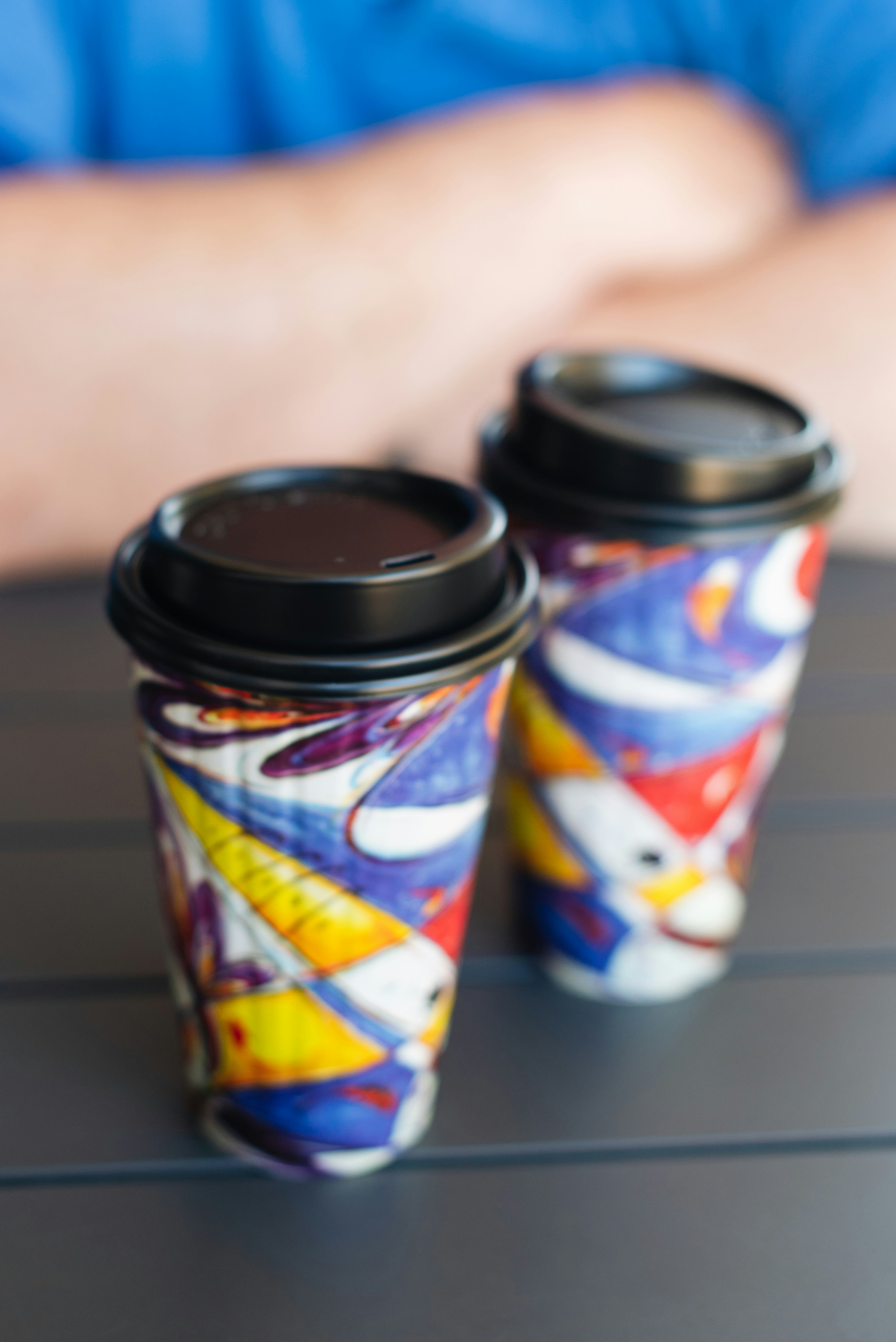 Colorful to-go cups in close-up blur with a blue-clad figure in the background