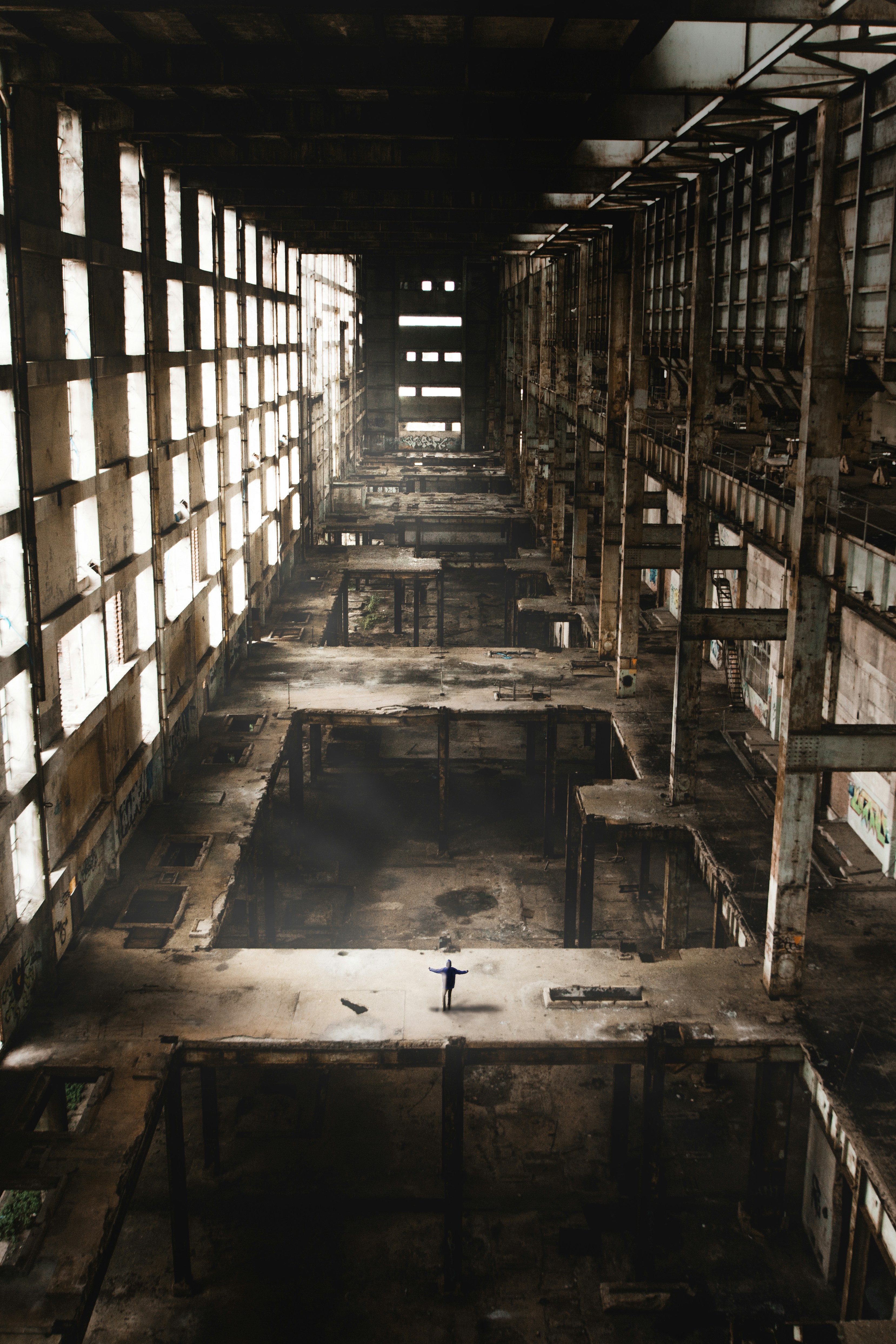 Lone Figure Beneath the Rusted Span in an Abandoned Factory Hall