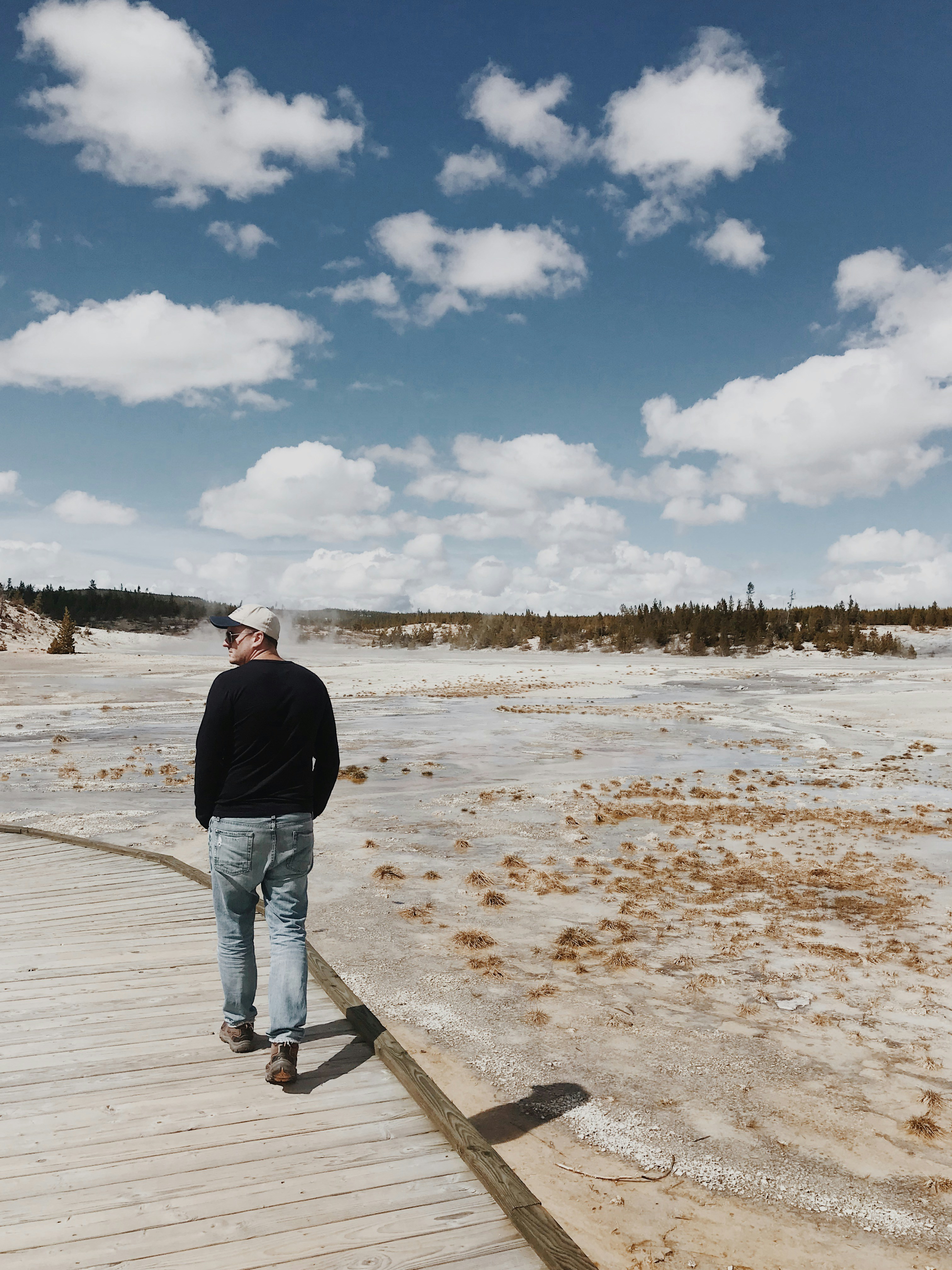 A solitary wanderer on a wooden boardwalk through a winter-barren plain under a puffy-blue sky