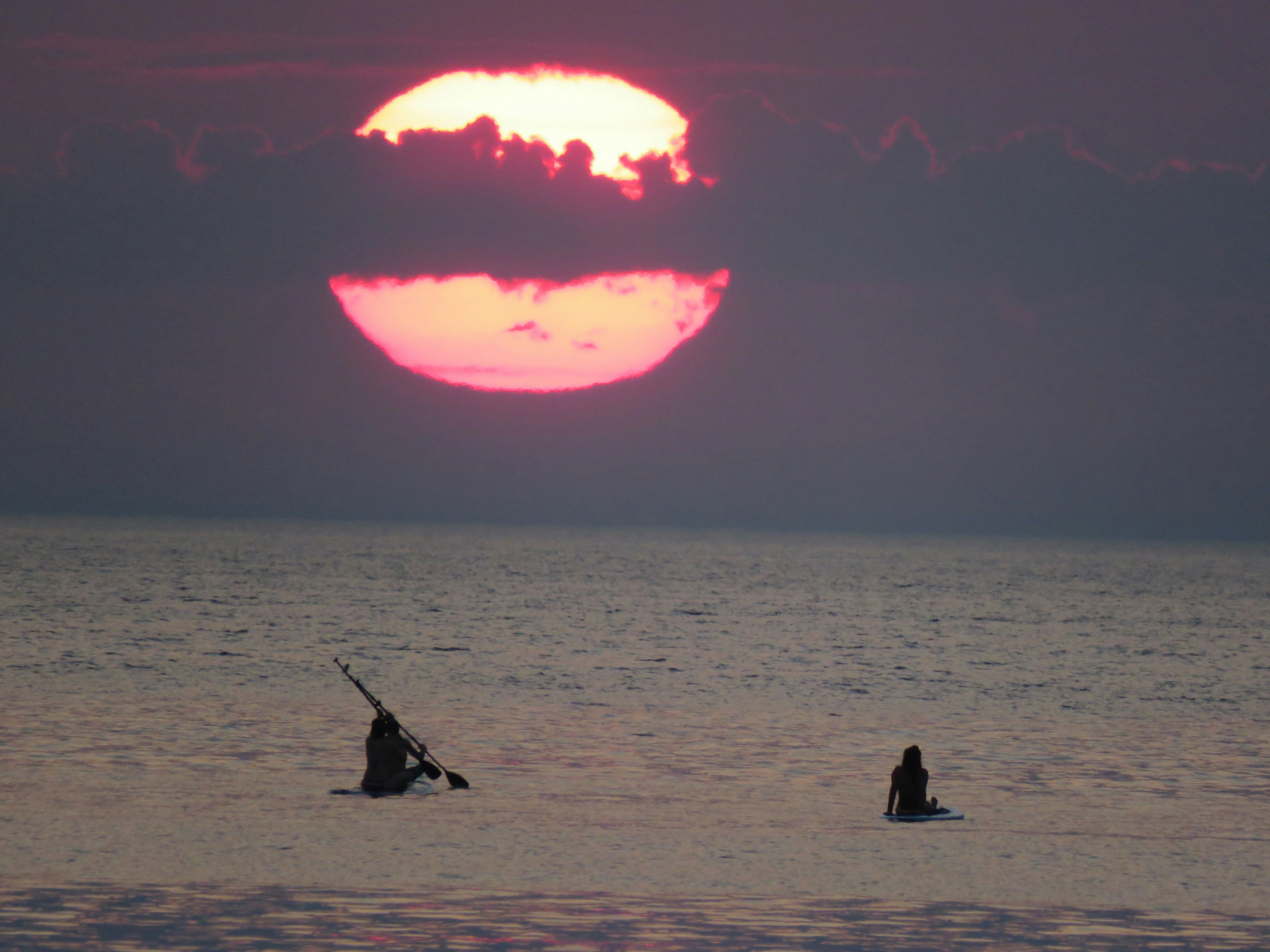 Crimson Horizon: Silhouetted Paddleboarders Against a Blushing Sunset