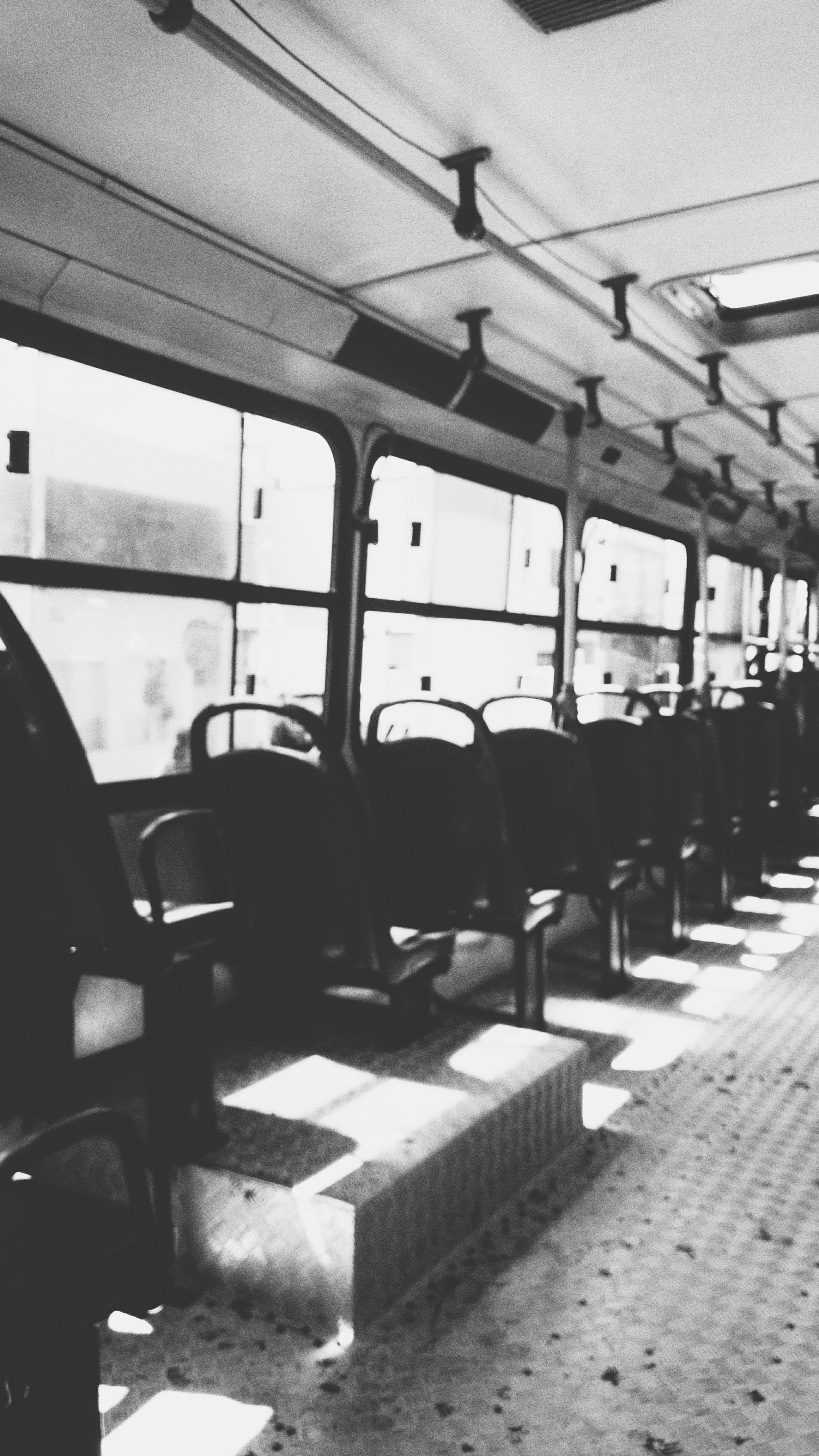 Black and white interior of an empty bus with sunlight streaming through the windows.