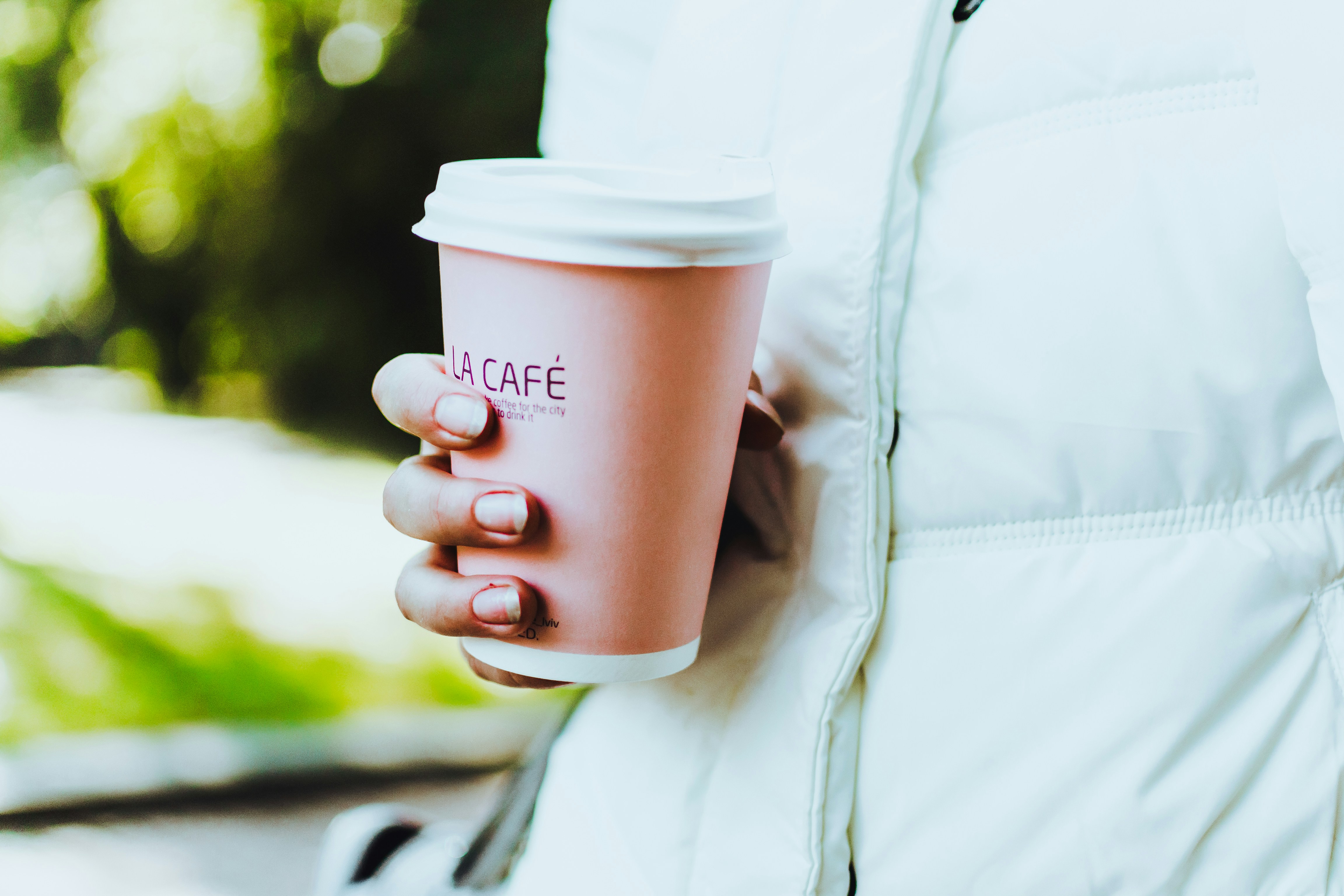 A Cozy Sip in Soft Focus: Coffee Cup Clutched in a Pale Park Moment