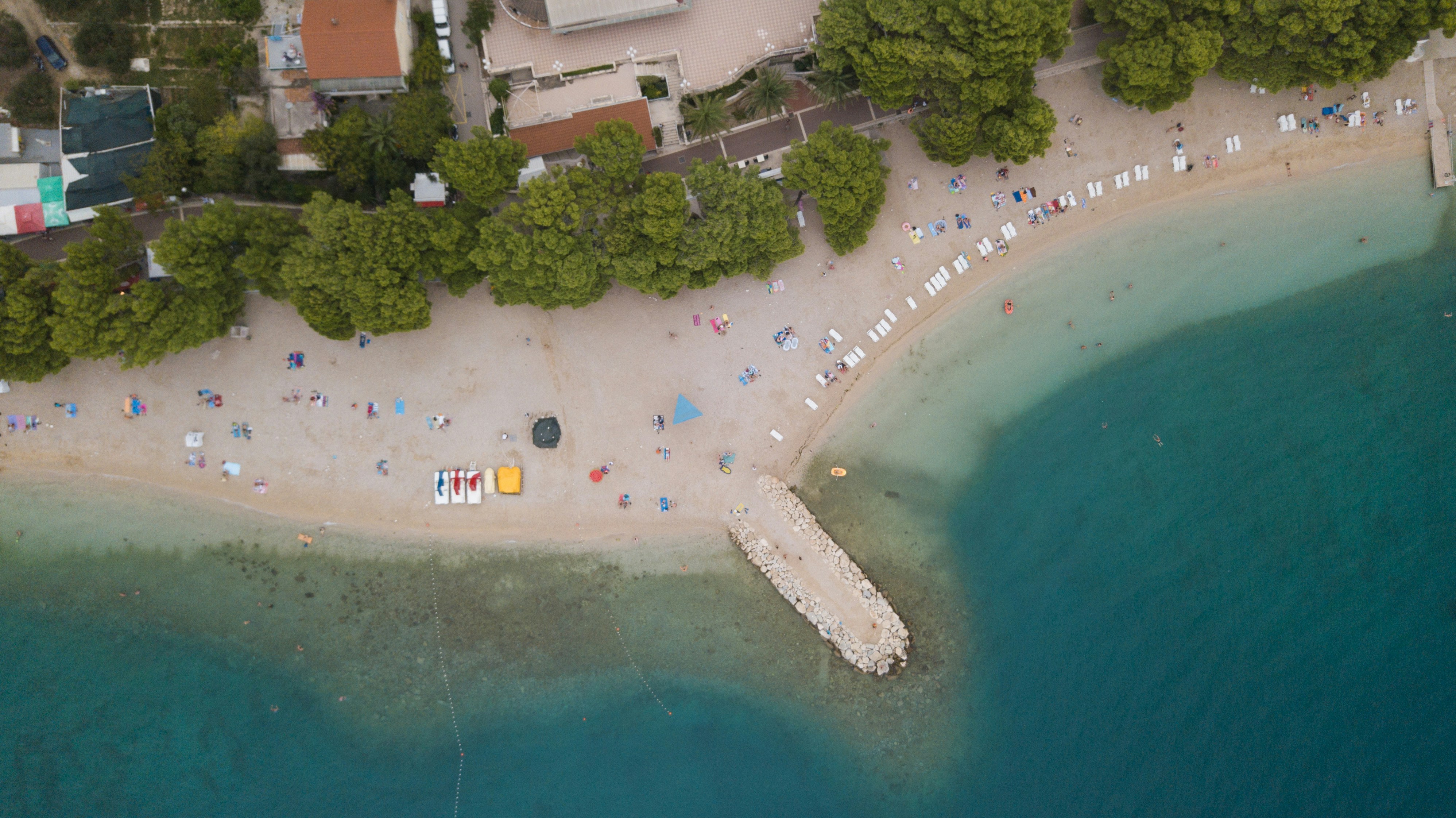Top-down view of a sandy beach bordered by turquoise waters and lush greenery.