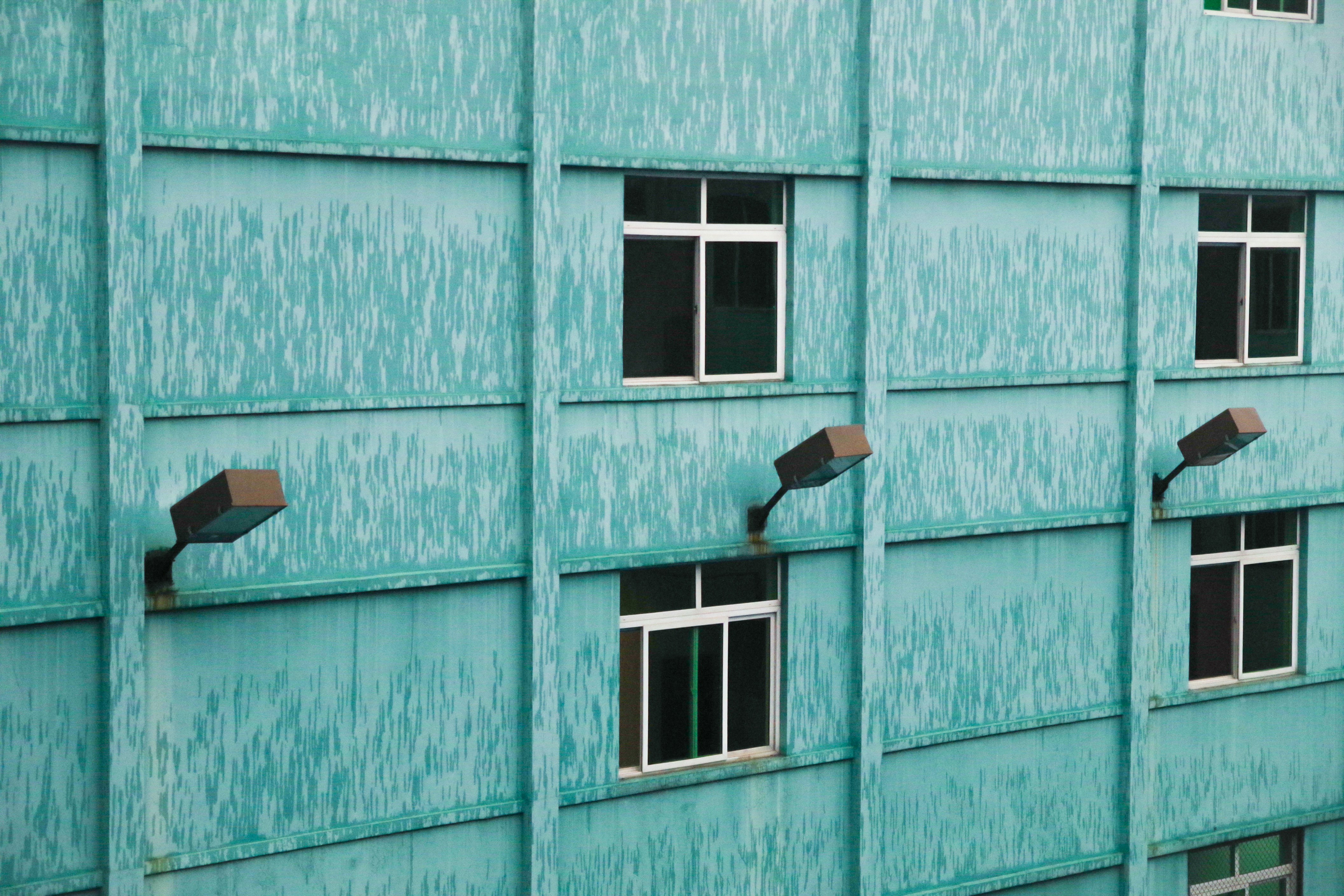 Teal Grid: Symmetrical Windows and Wall Lamps on a Weathered Facade