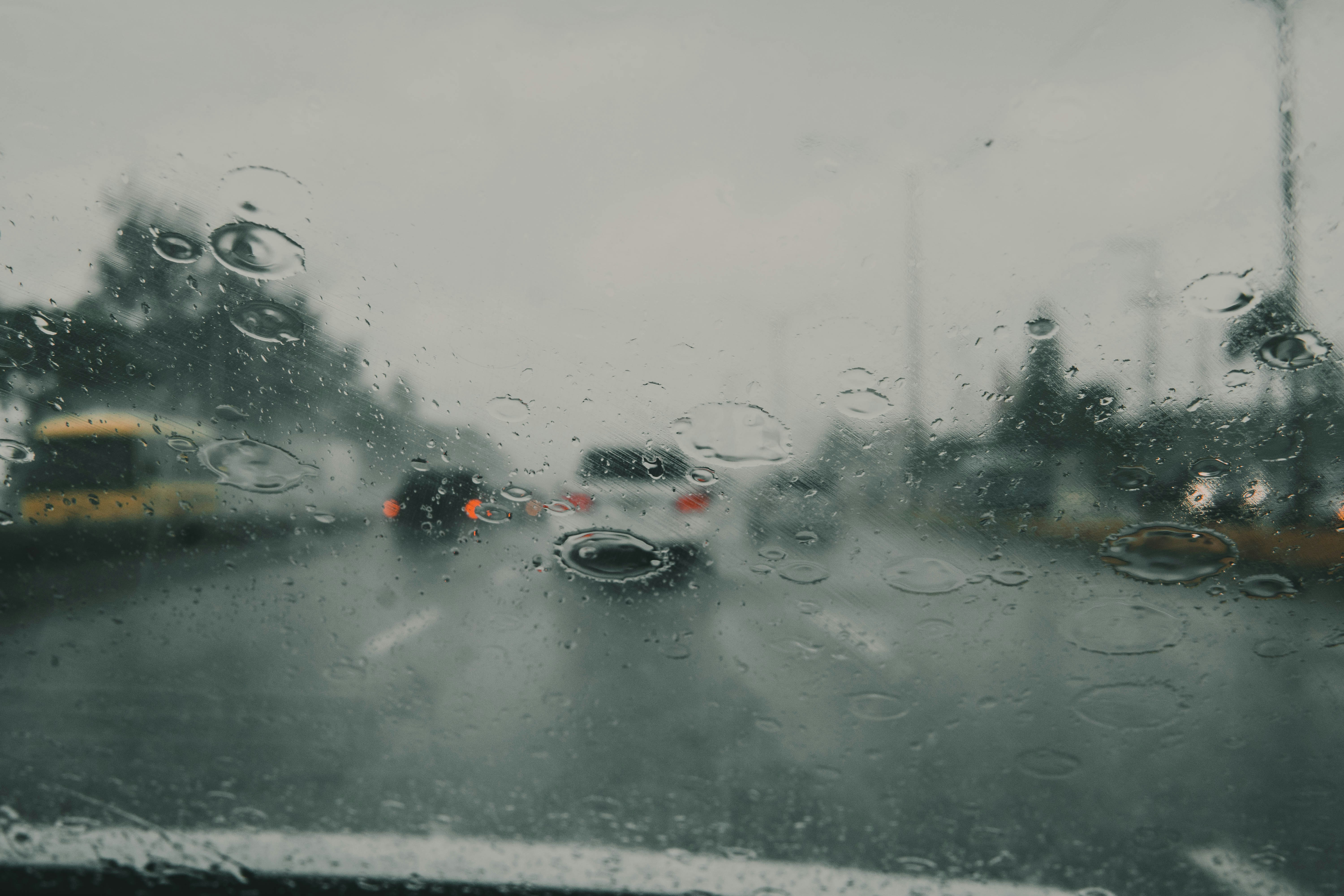 Raindrops cascade over a car windshield, blurring the view of a busy city street during a downpour.