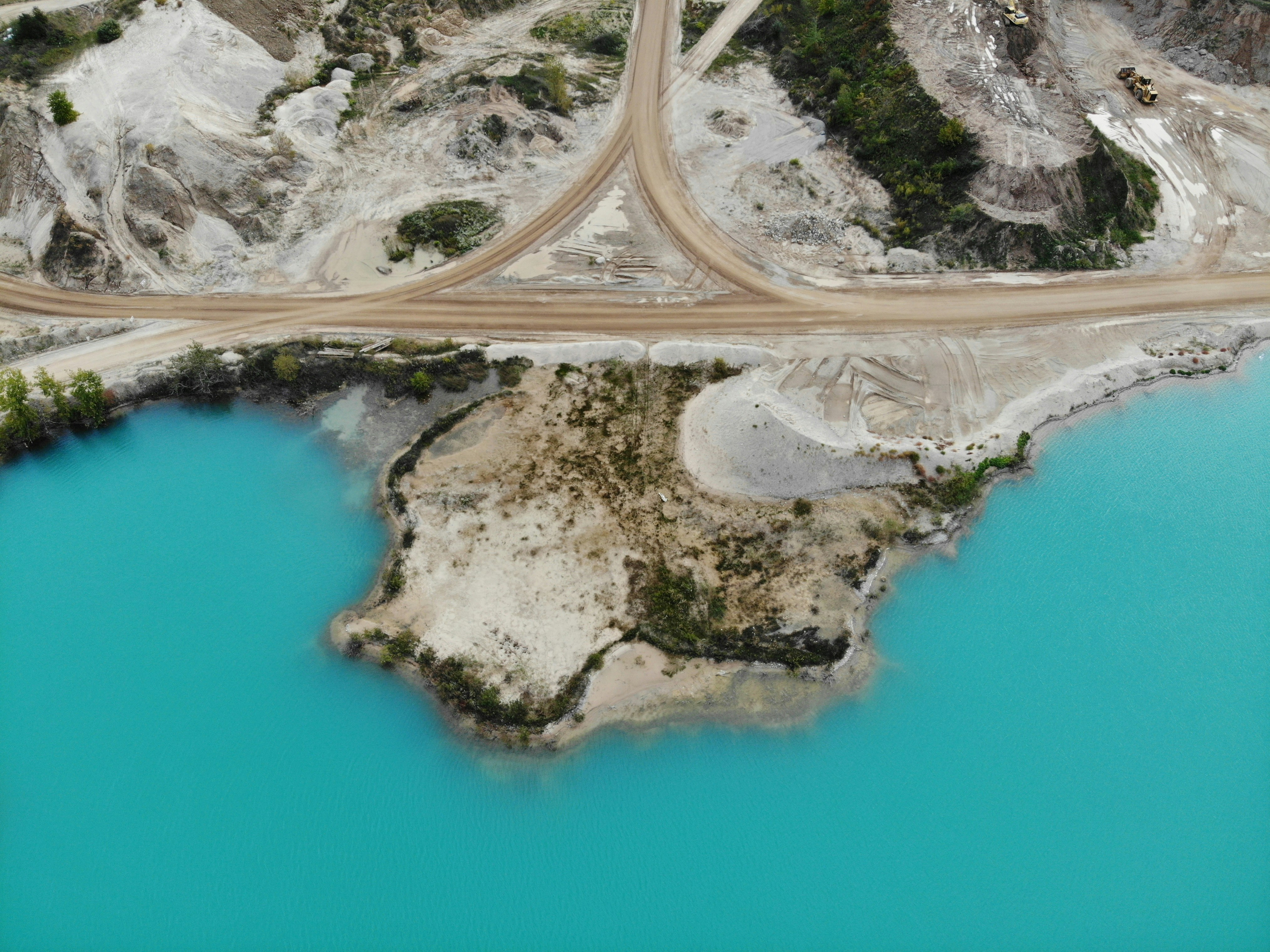 Aerial view of a turquoise lagoon bordered by sandy shores and rugged terrain, showcasing the contrast between natural beauty and industrial activity.
