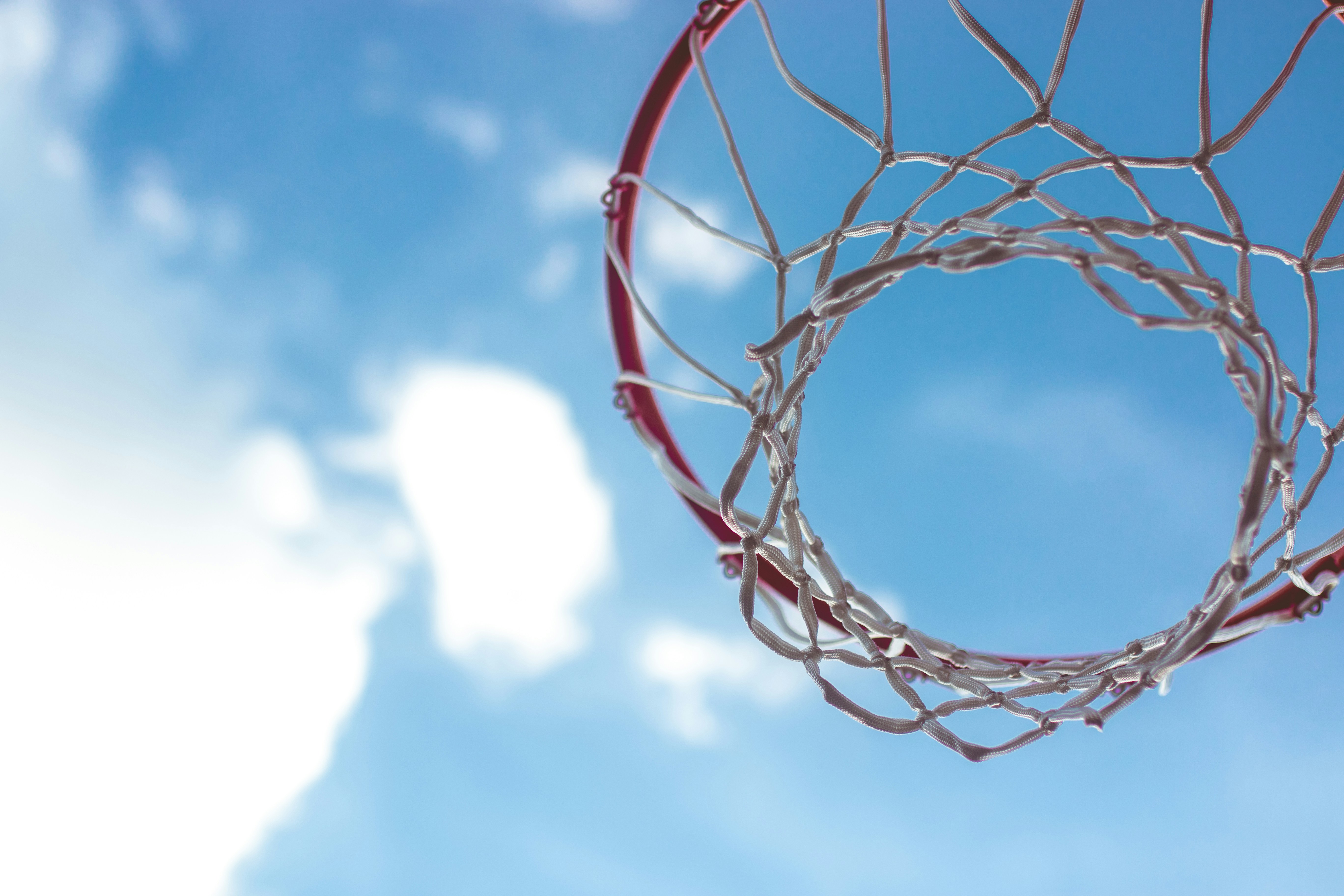 Red basketball hoop set against a clear blue sky with scattered clouds.