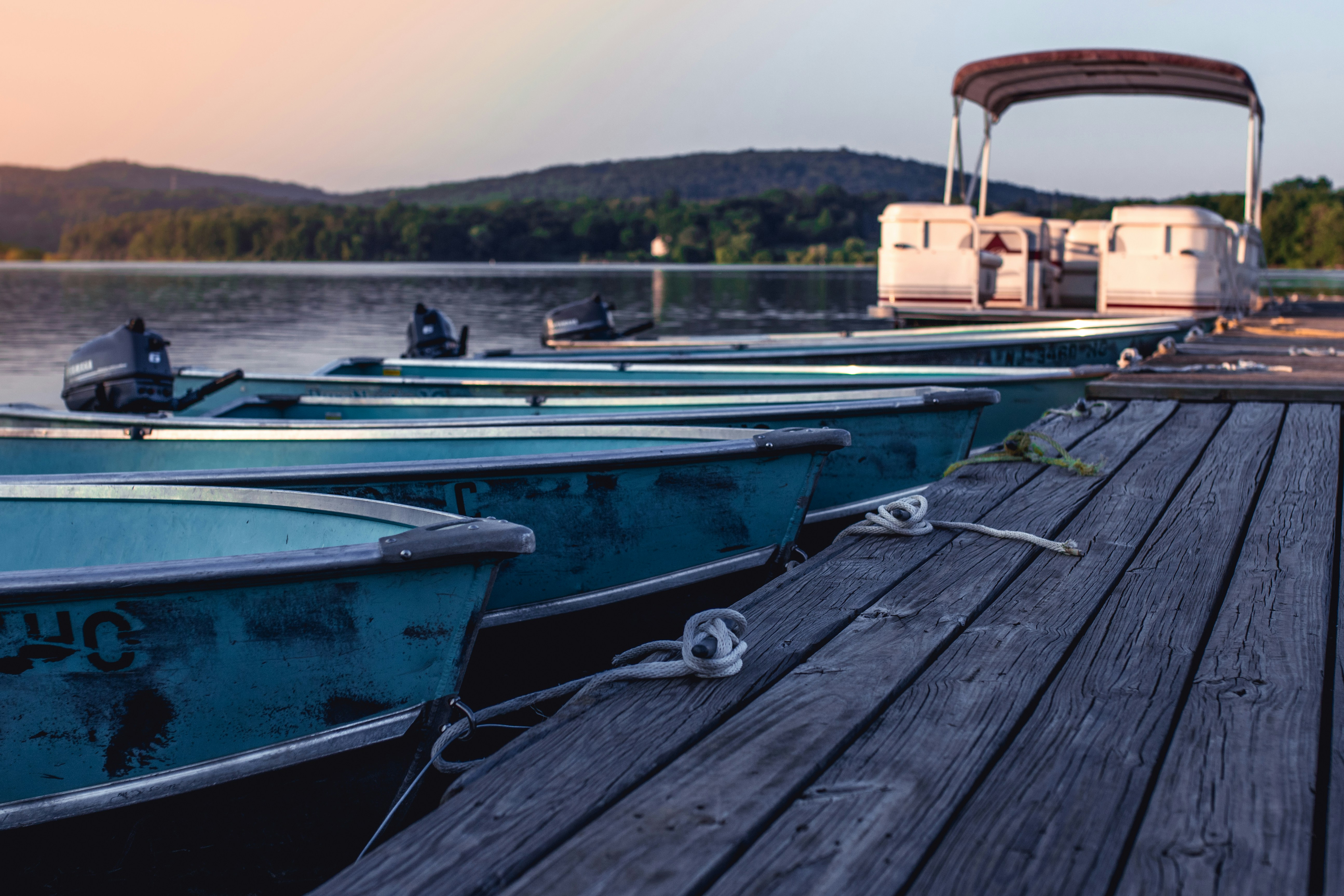 Rowboats lined up on a wooden dock at sunset with distant hills in view.