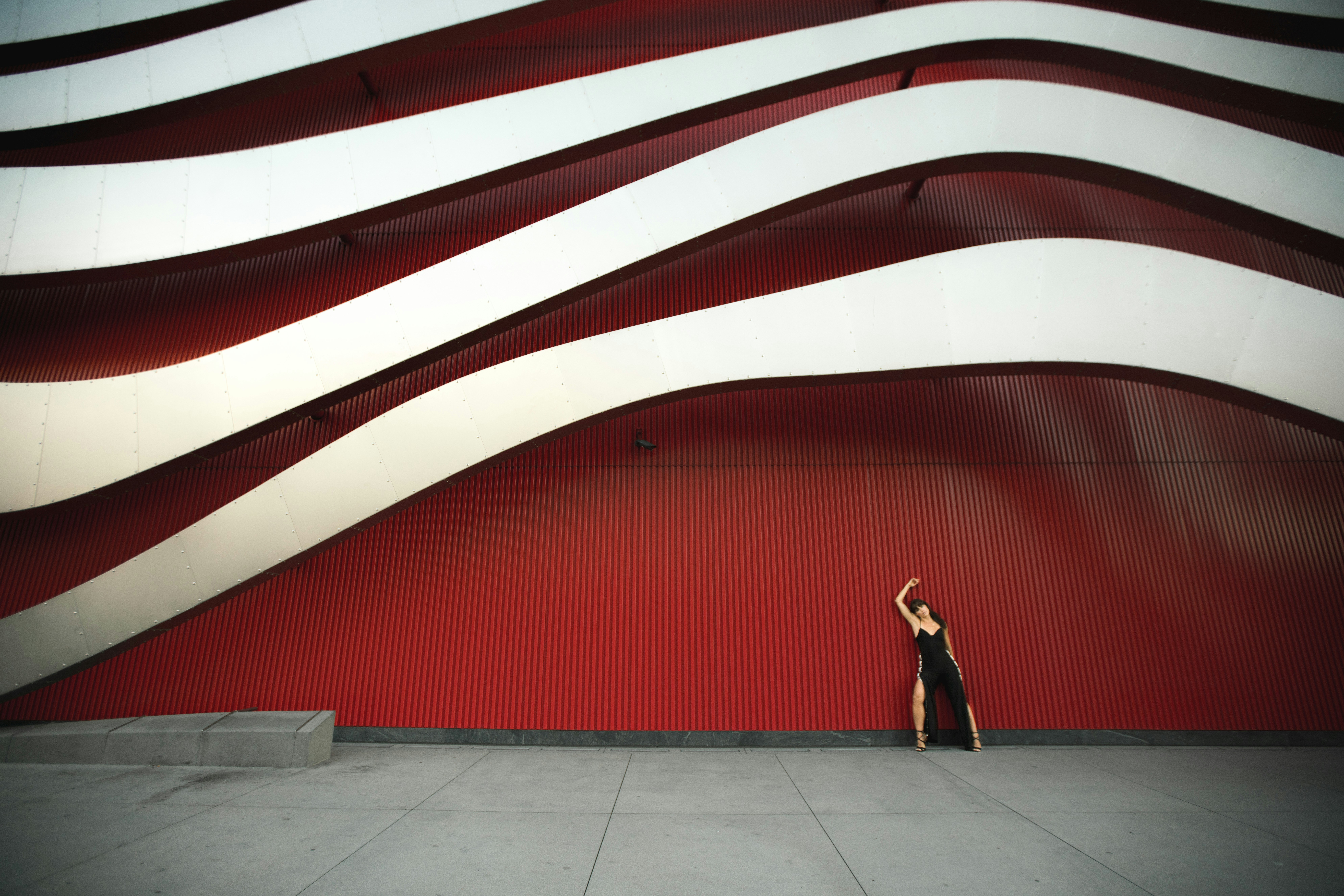 A dancer poses gracefully against a backdrop of curving red and white architectural panels, highlighting the interplay of movement and structure.