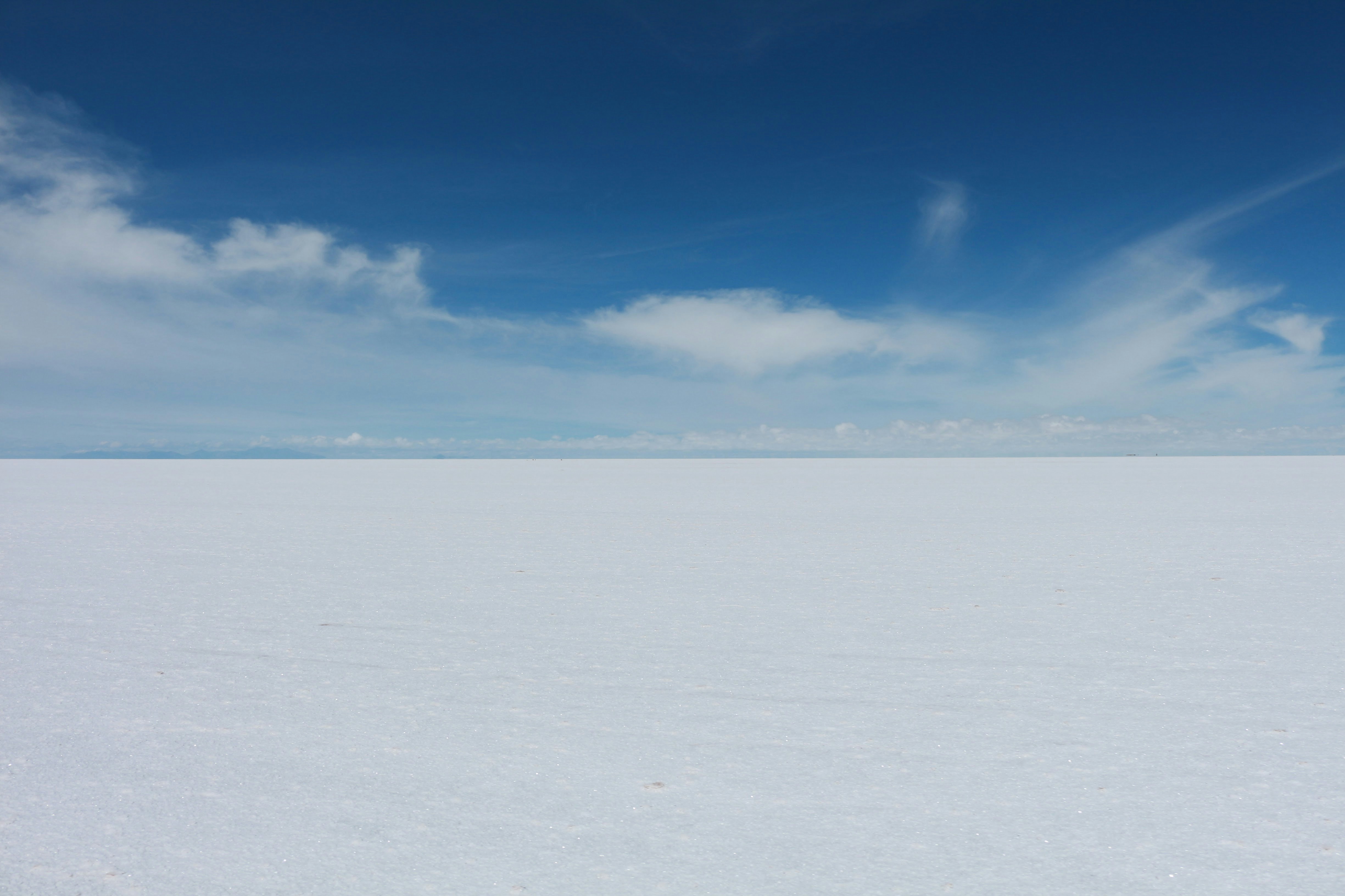 Vast salt flat under a clear blue sky, showcasing a seamless blend of earth and sky. The horizon stretches infinitely, creating a tranquil scene.