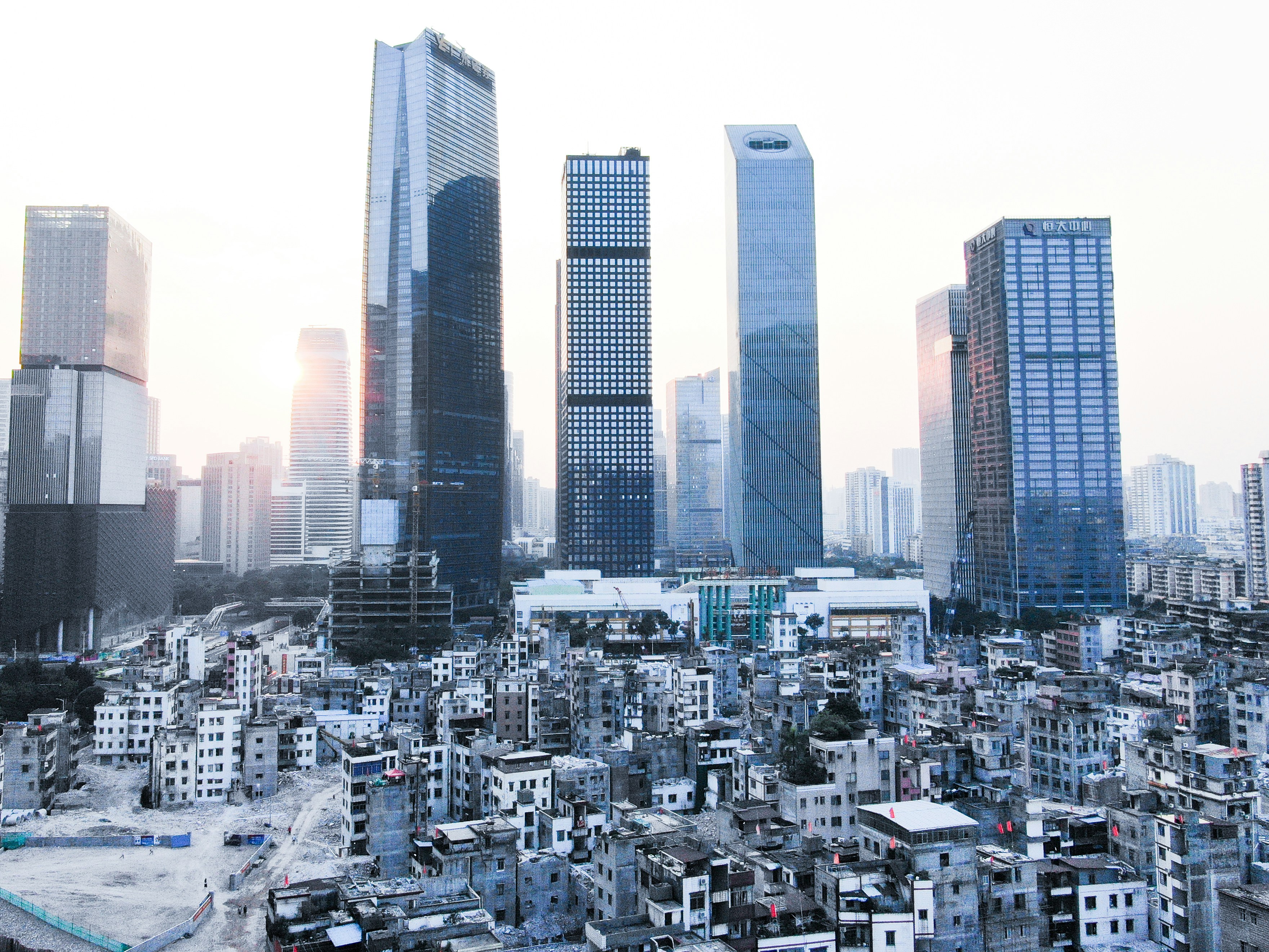 Skyscrapers towering over densely packed older buildings in a cityscape at dusk.