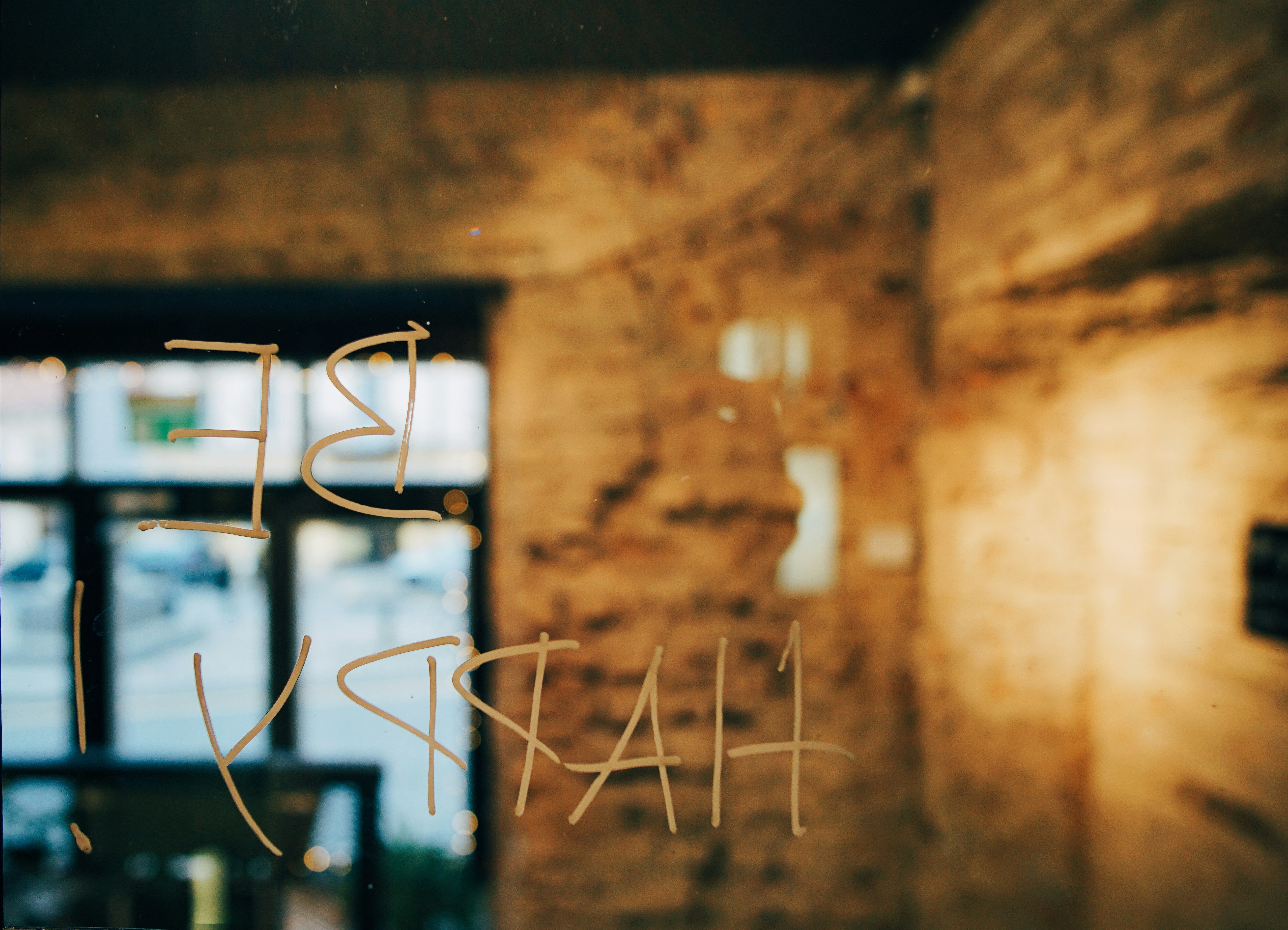 Message scrawled on a glass pane with a blurred brick interior backdrop.