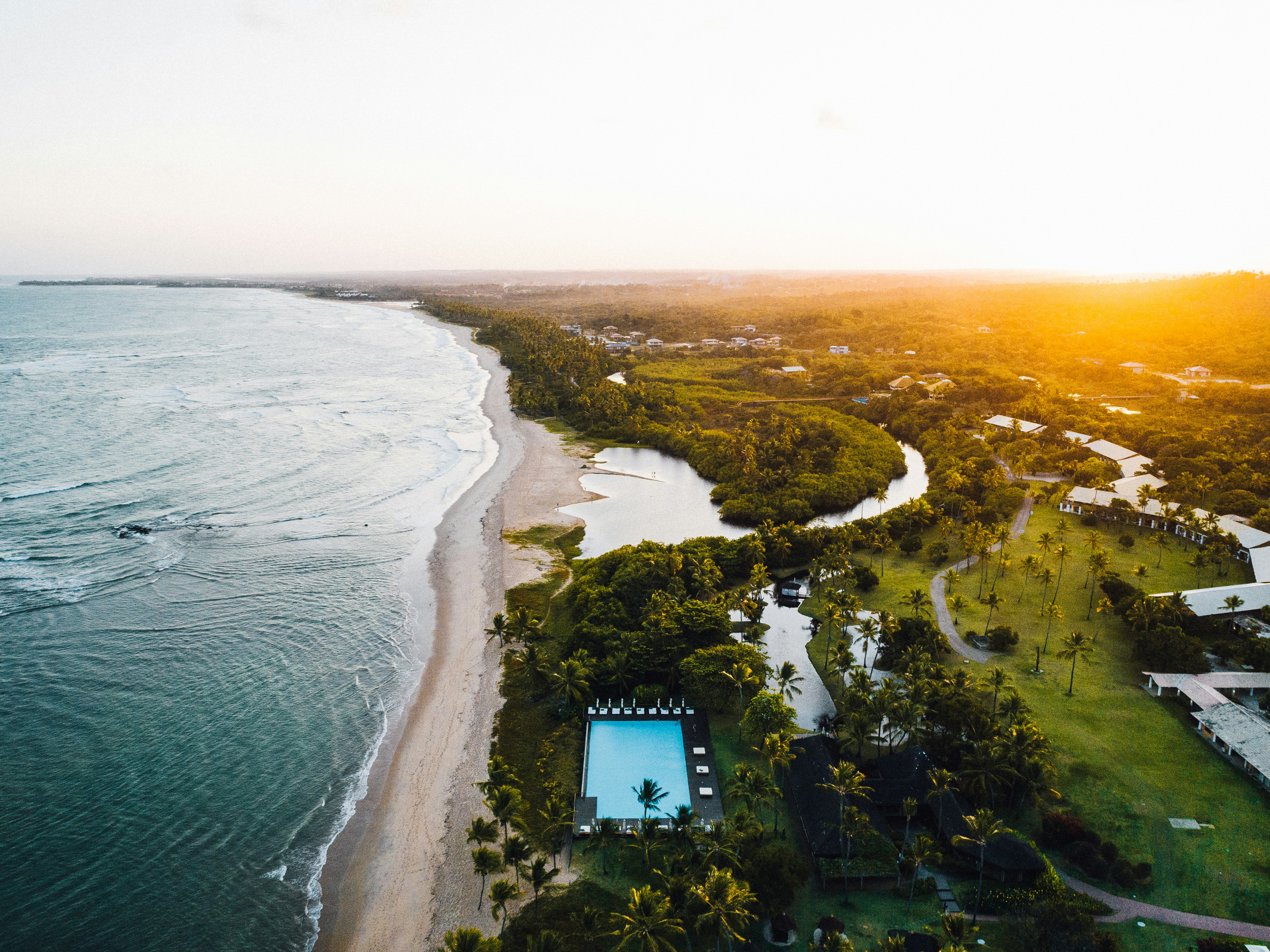 Aerial view of a coastline stretching alongside lush greenery at sunset.