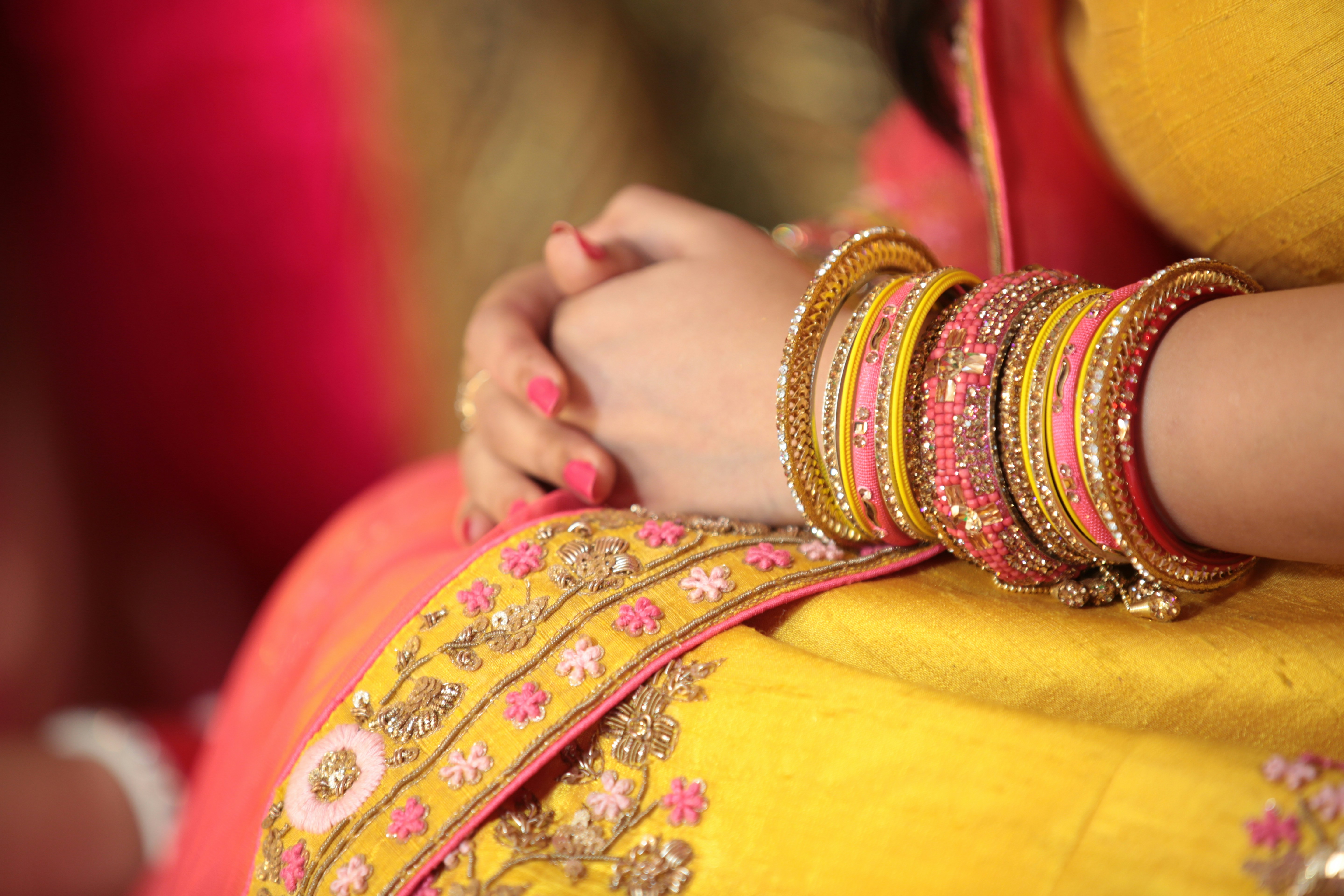Close-up of adorned hands with vibrant bangles resting on a traditional outfit, showcasing intricate embroidery. The scene reflects cultural richness and festive spirit.