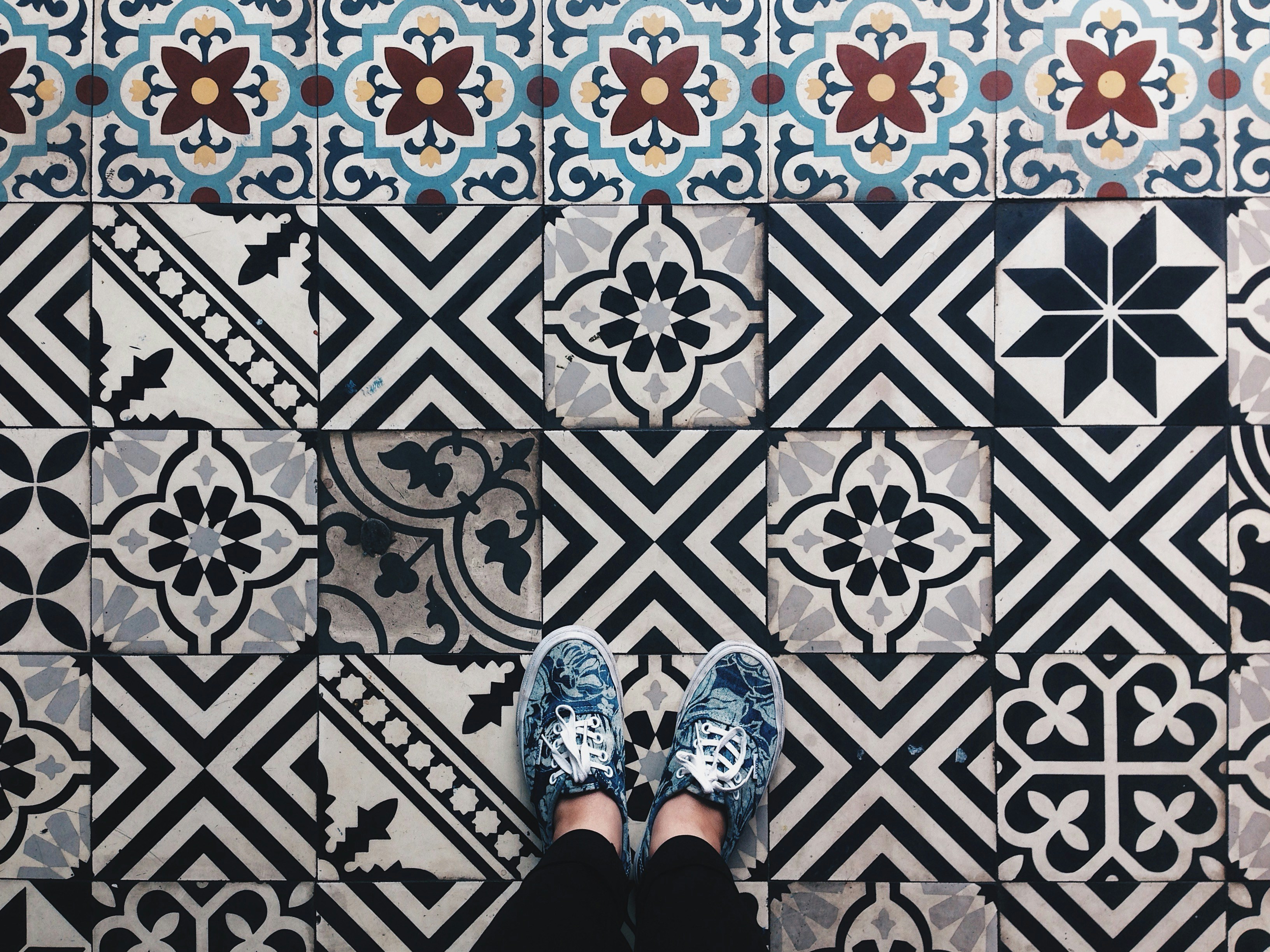Sneakers on intricately patterned black and white tiles with colorful designs in the background.