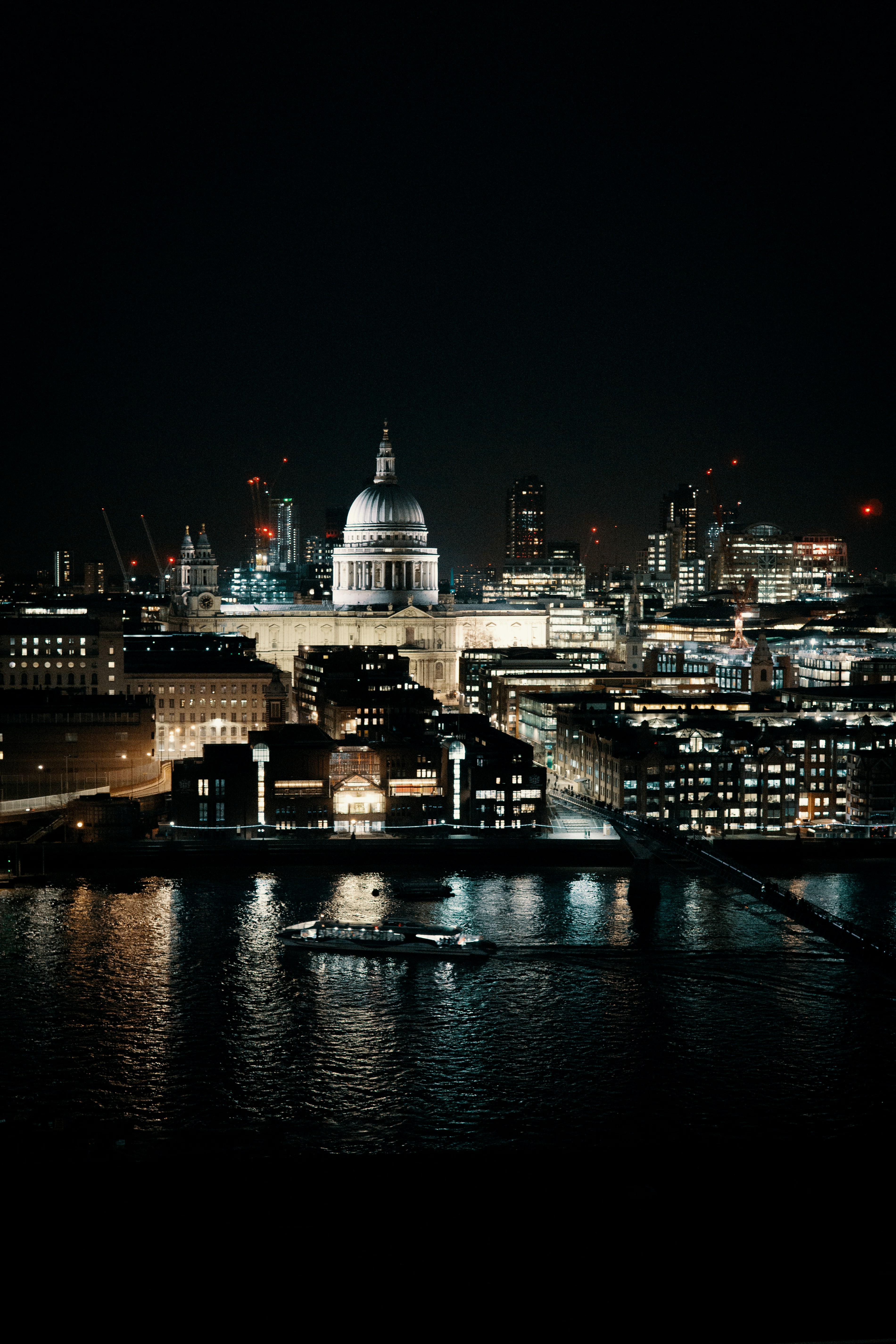 Illuminated St. Paul's Cathedral stands majestically against a backdrop of London's skyline at night, reflecting on the Thames River.